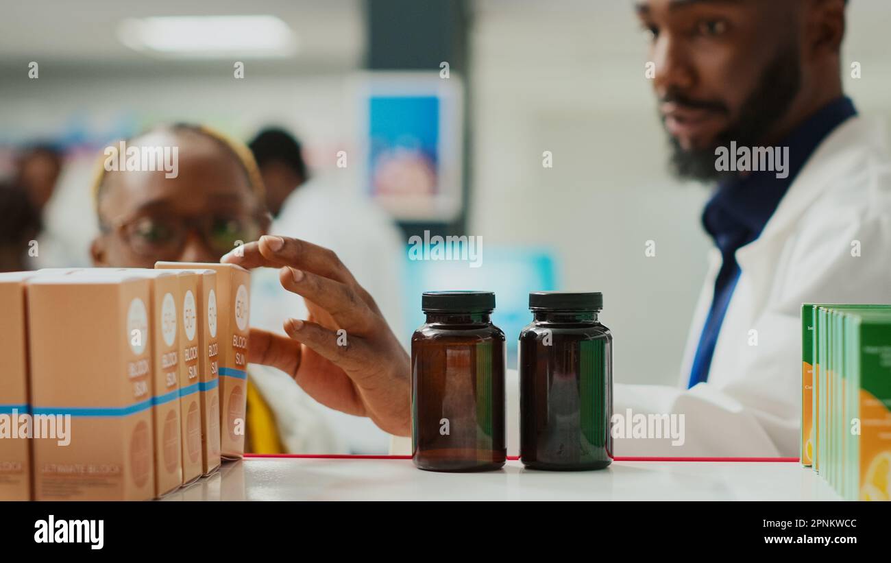 Male assistant showing bottle of pills to customer in pharmacy ...