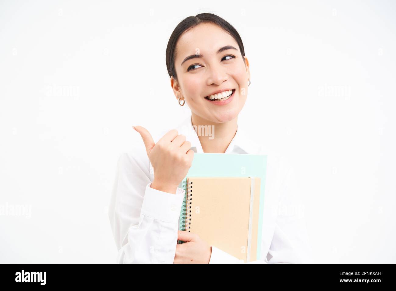 Image of smiling asian woman with notebooks, pointing left and looking ...
