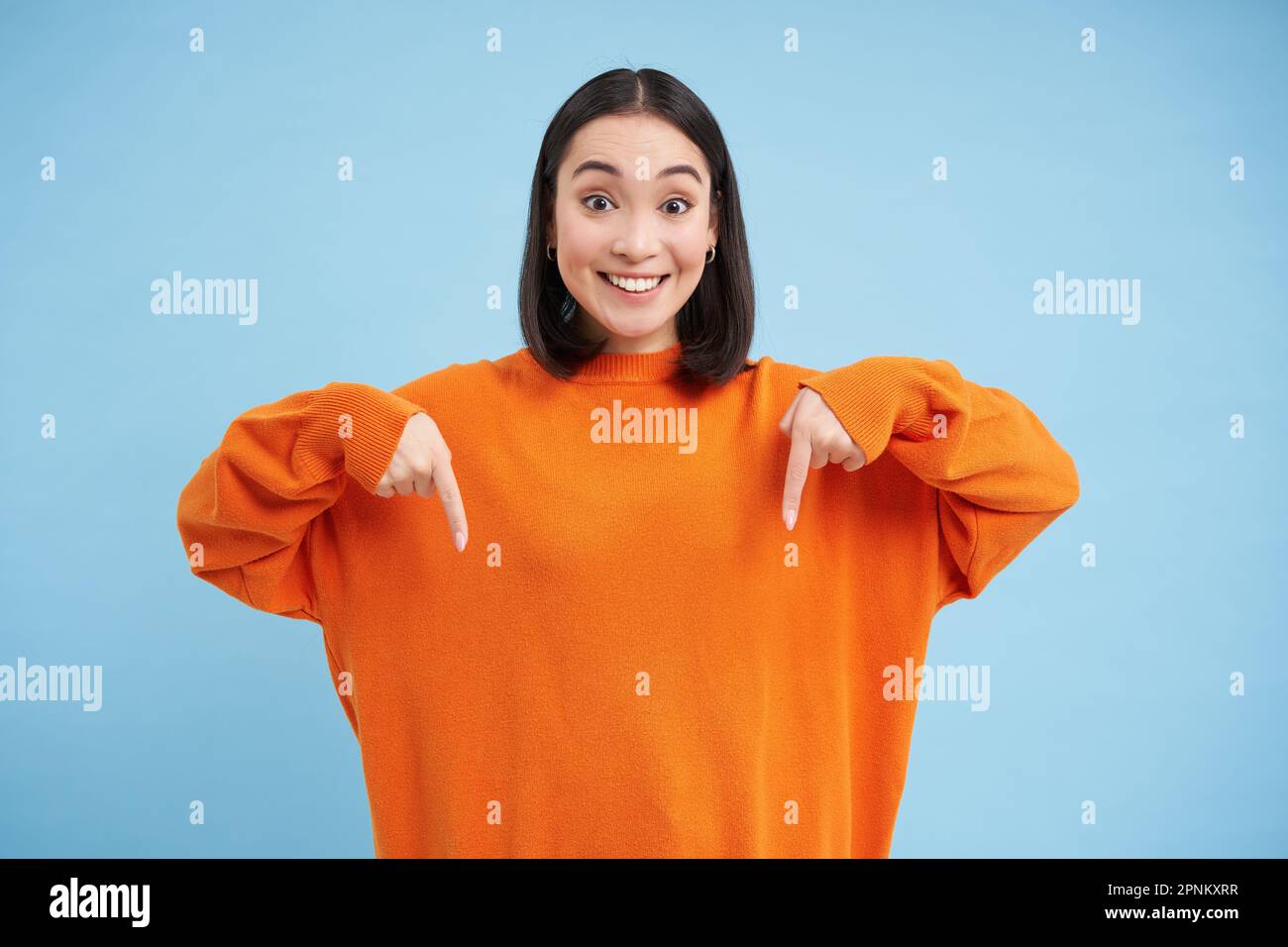Excited asian woman pointing down, shows advertisement below with happy ...