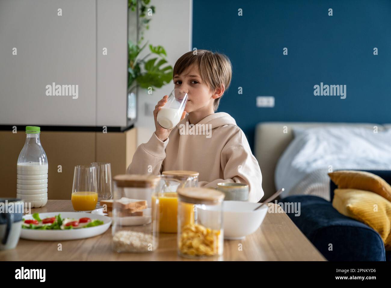 Pleased kid boy look at camera sits at kitchen table drink glass of ...