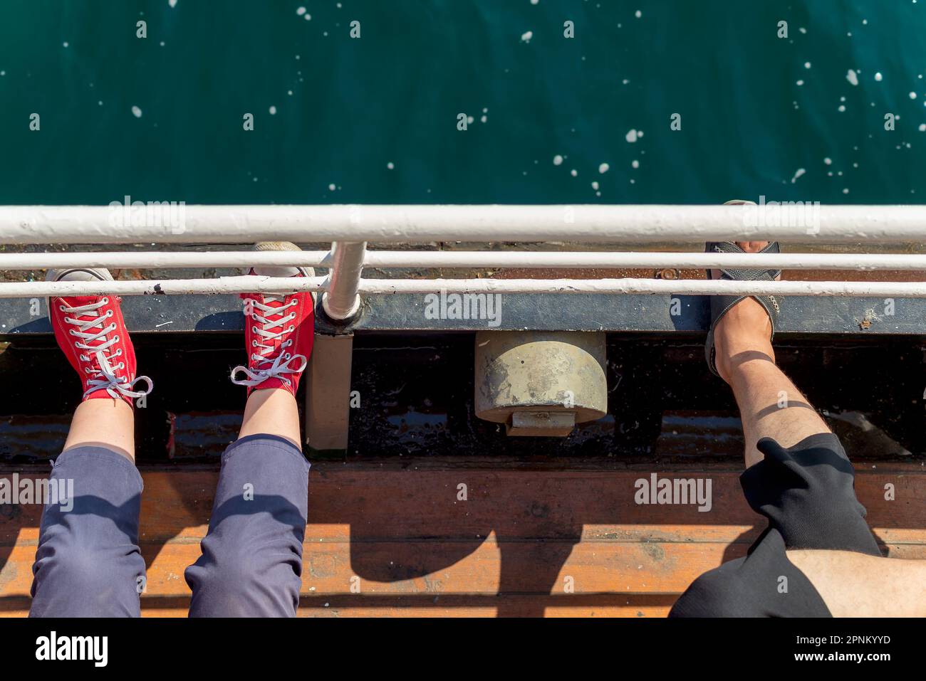 Top view showing legs of two persons, sitting on a narrow sea side ...