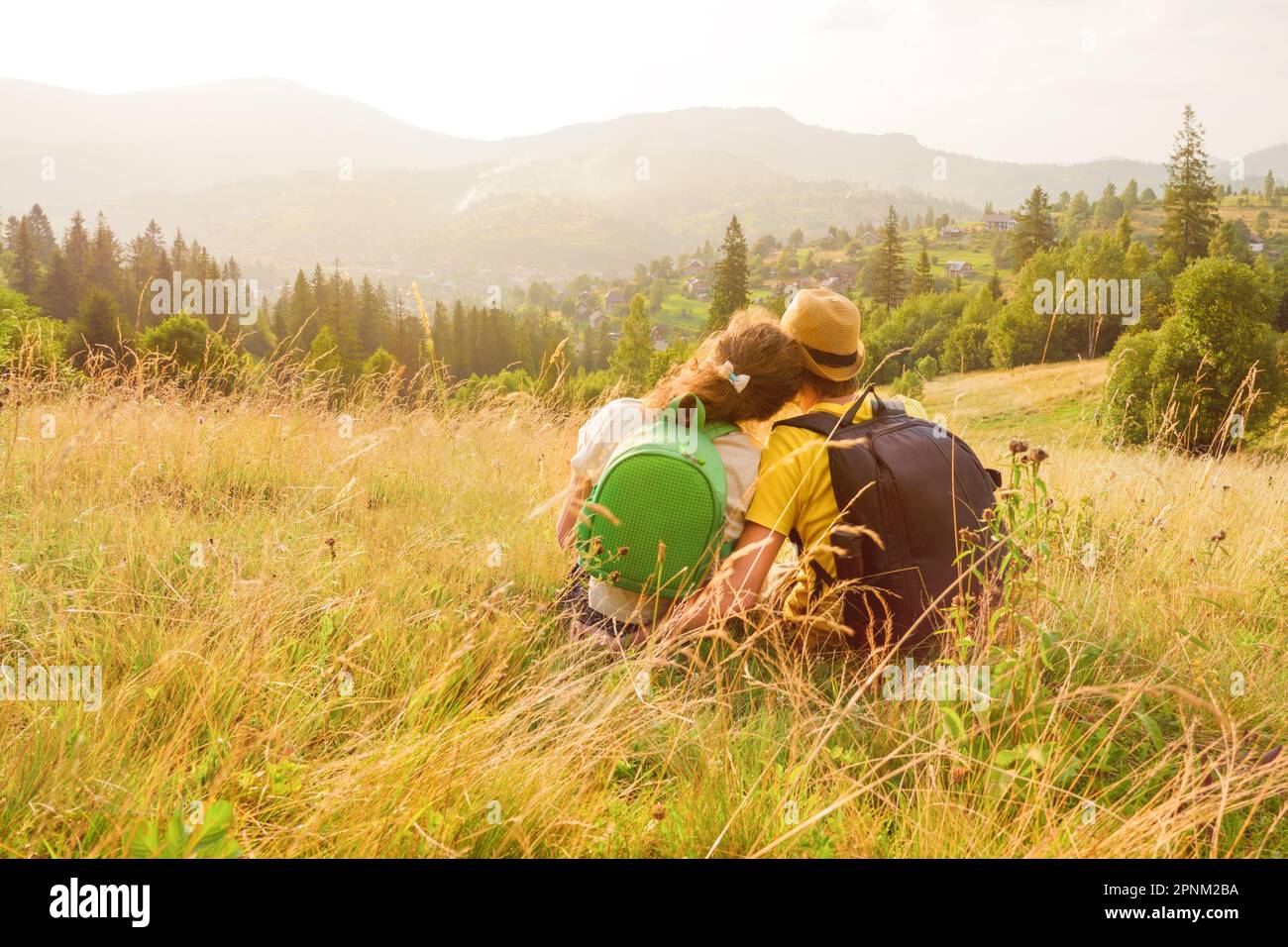 Back view. Happy young couple sitting on mountain couple looking at ...
