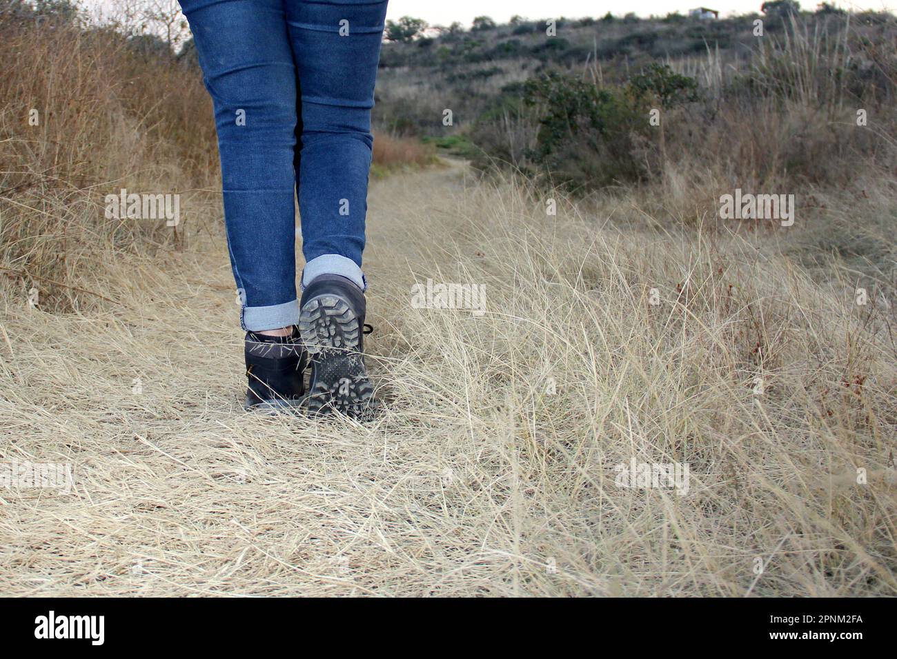 Legs with denim pants and black hiking boots in the middle of the field ...