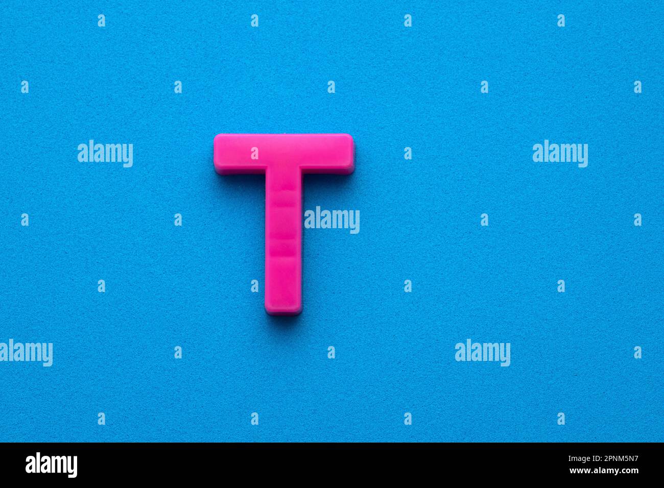 Alphabet letter T - Pink plastic piece on blue foamy background Stock ...