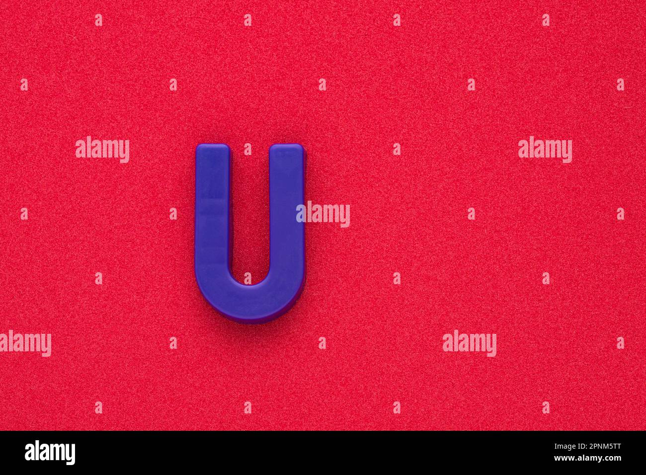 Plastic letter U uppercase in violet color on a red 032 c foamy ...