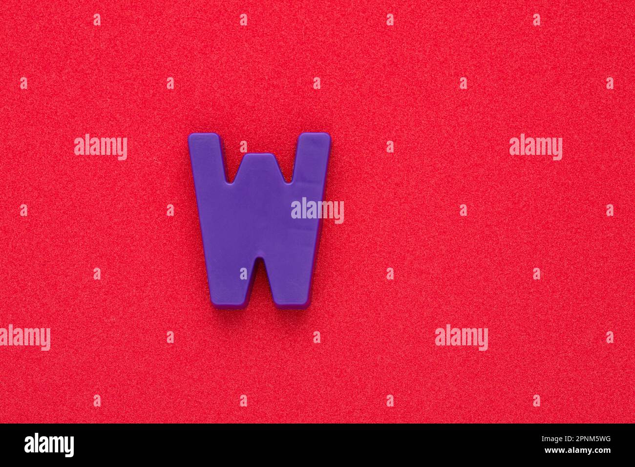 Plastic letter W uppercase in violet color on a red 032 c foamy ...