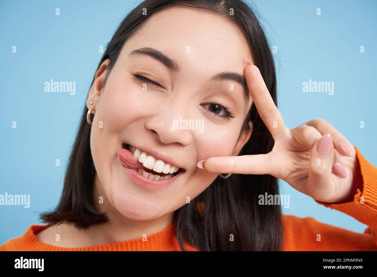 Close up portrait of positive asian woman, winks and shows peave, v ...