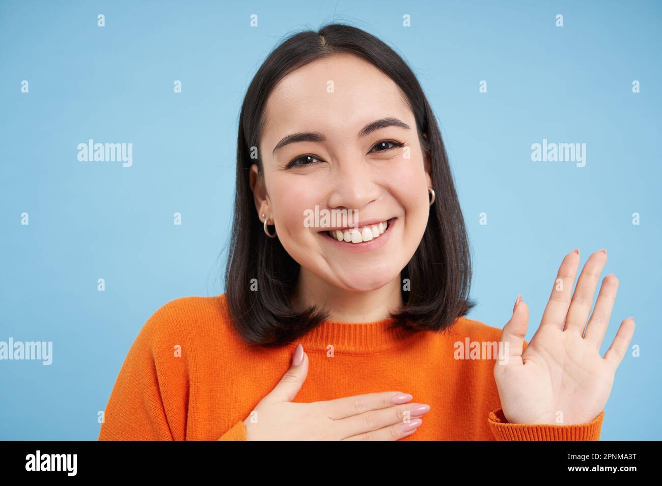 Close up of friendly smiling japanese woman, raises one arm, introduce ...