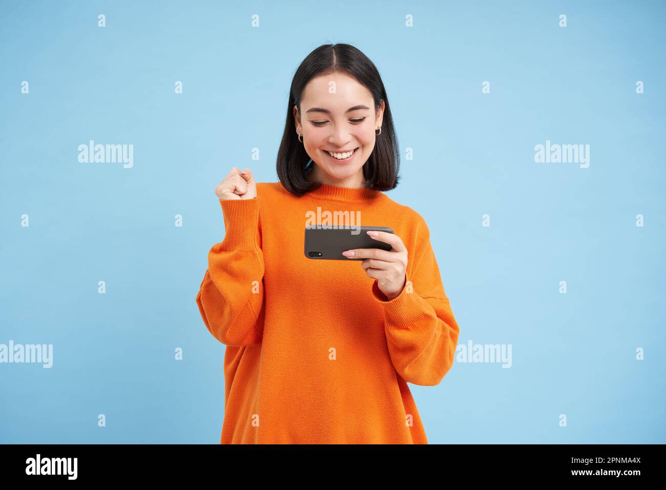 Happy korean girl winning on mobile phone video game, holding cellphone ...