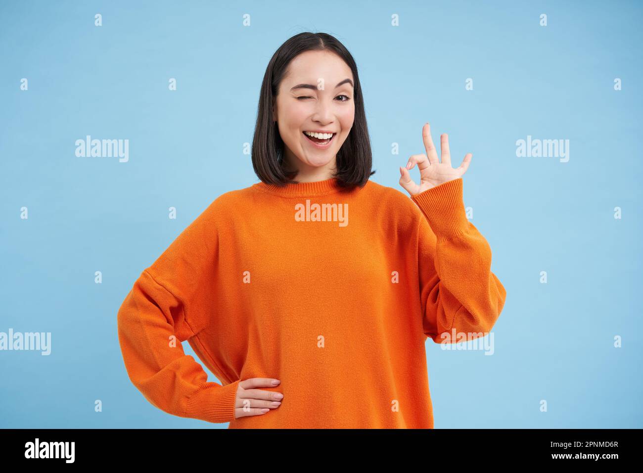 Alright, very good. Smiling winking girl, asian woman shows okay sign ...