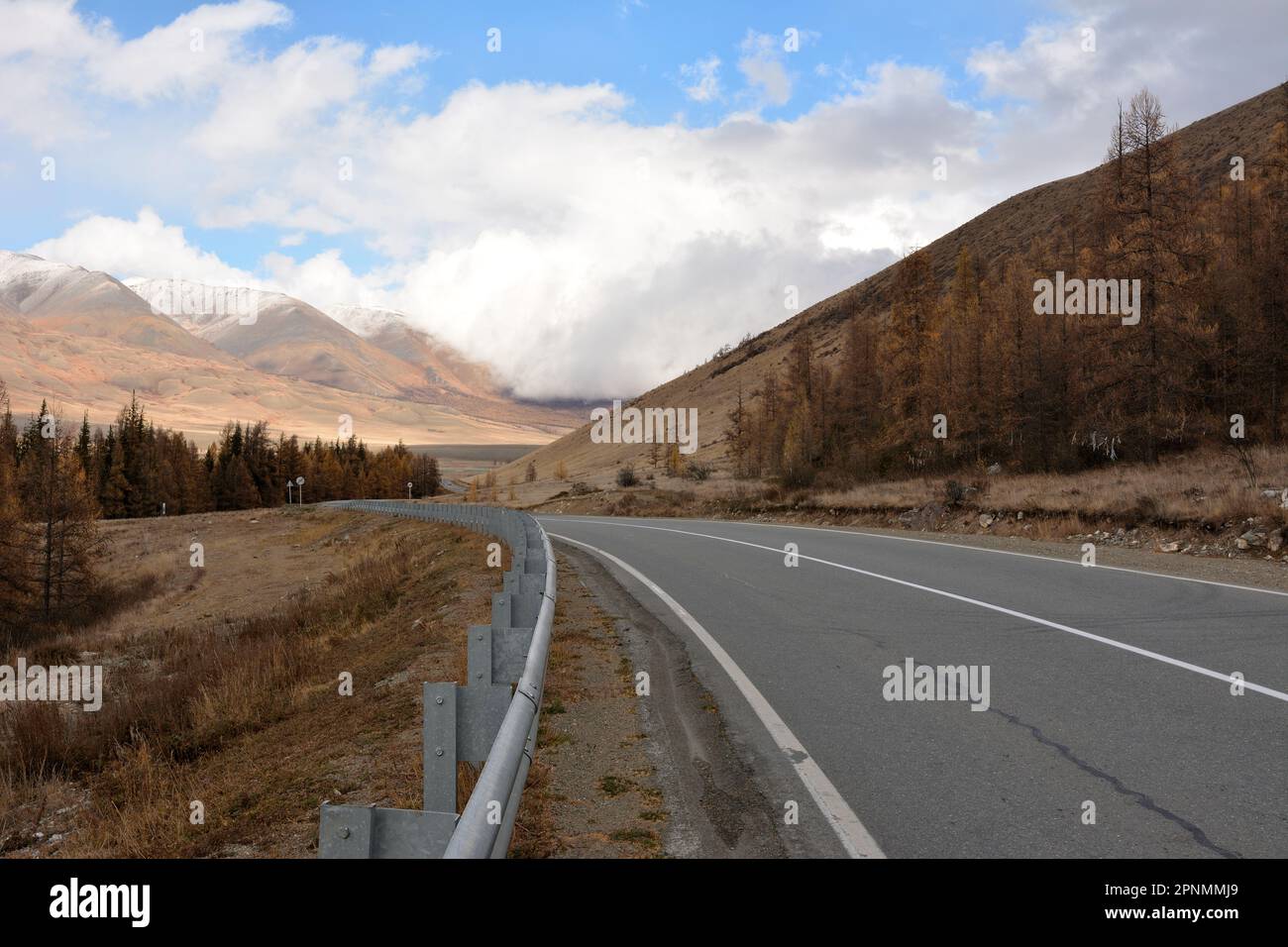 The turn of a two-lane asphalt road with fences descends from a hill ...