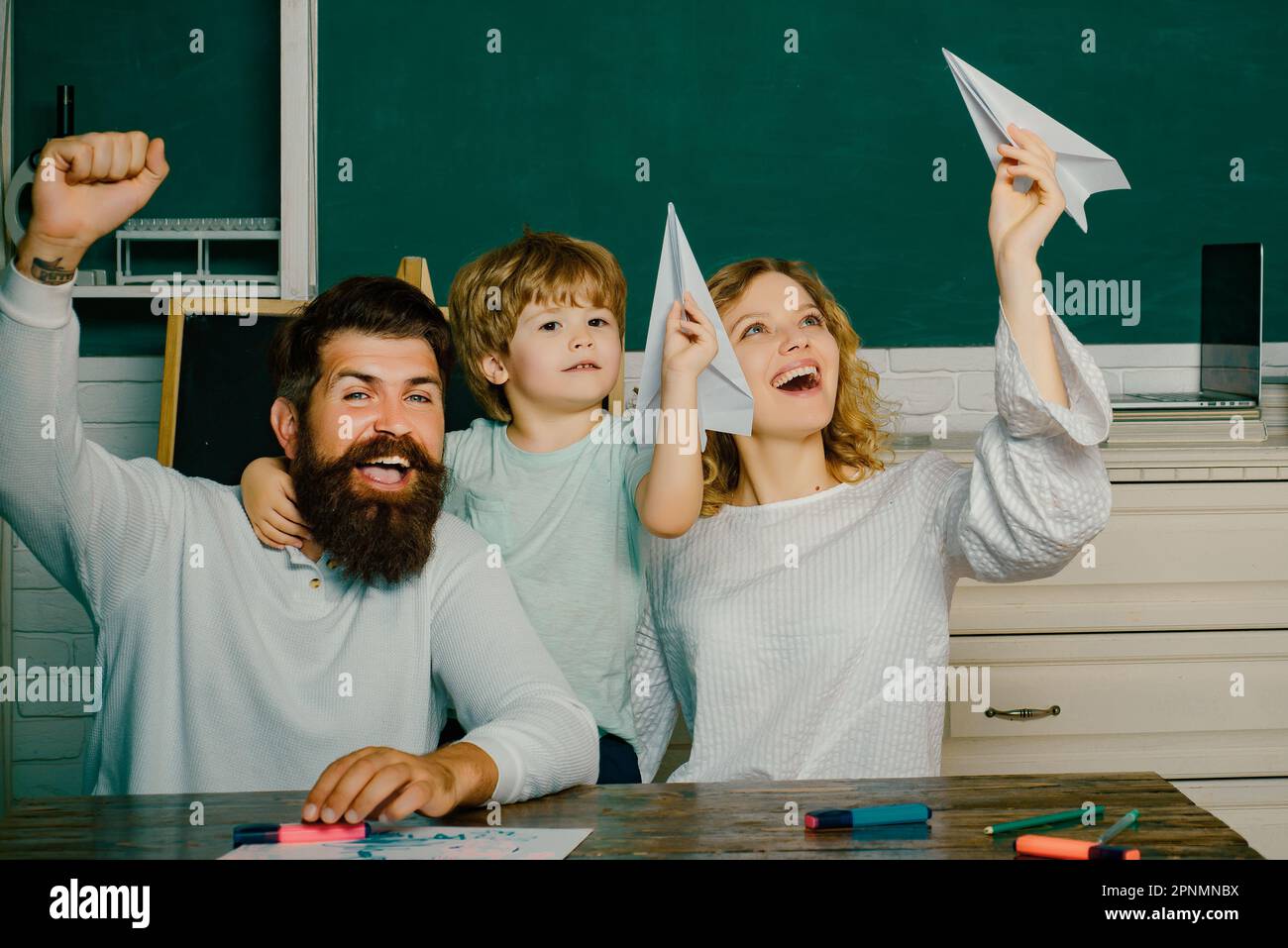 Pupil with paper airplane playing with parents. Young couple helping ...