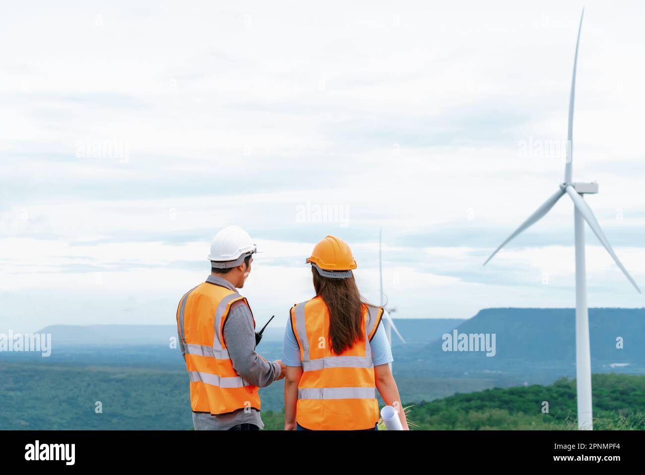 Male and female engineers working on a wind farm atop a hill or ...