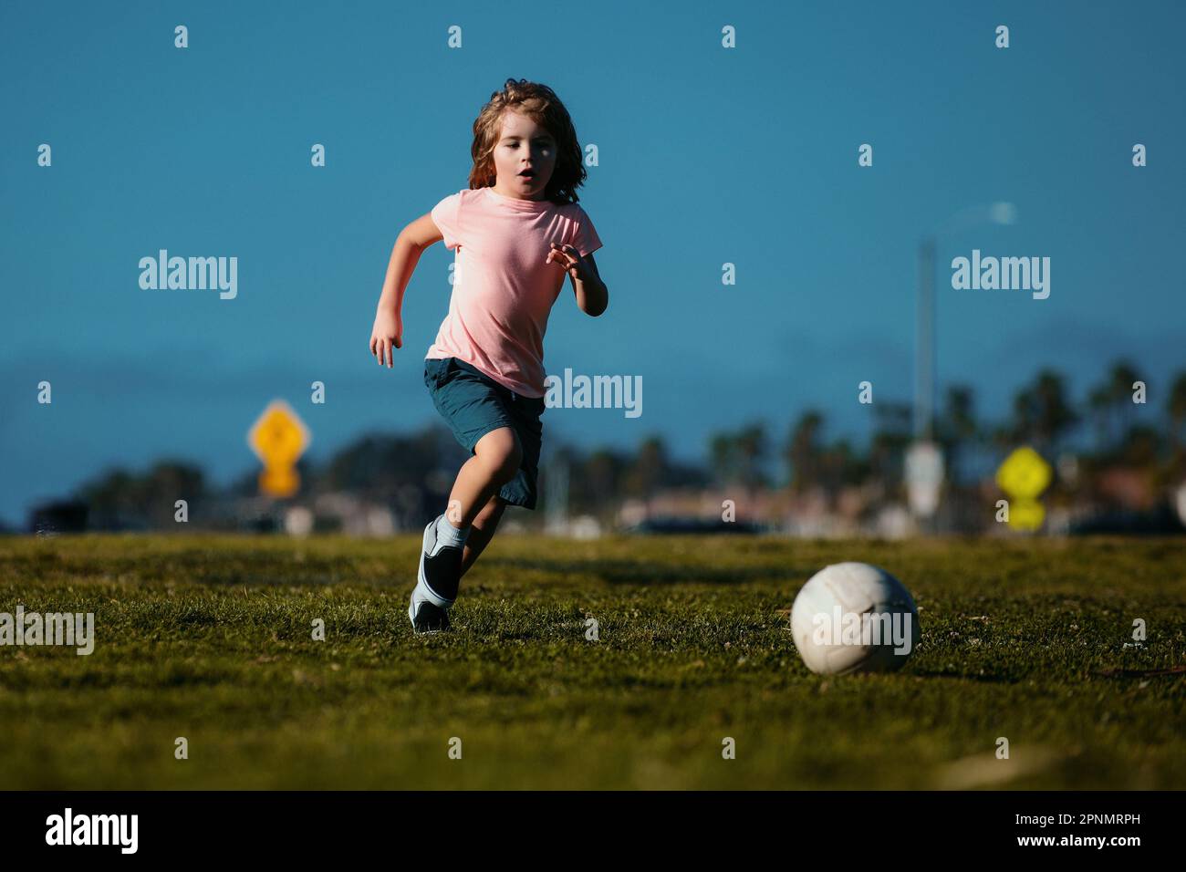 Excited child boy kicking ball in the grass outdoors. Soccer kids ...