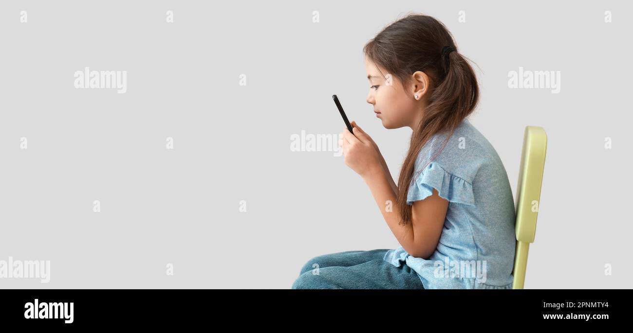 Little girl with bad posture using mobile phone on light background ...