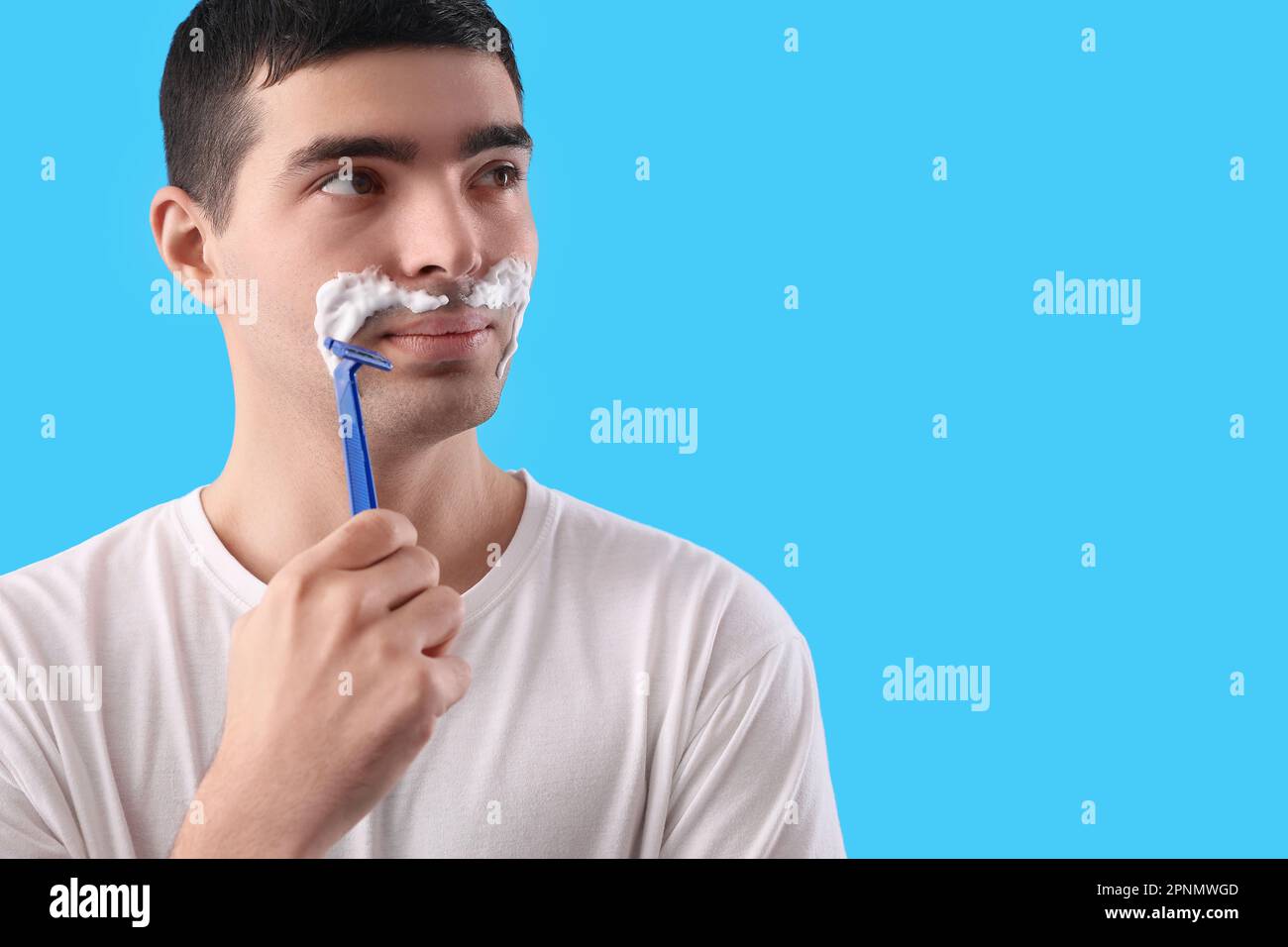 Young man shaving against light blue background Stock Photo - Alamy