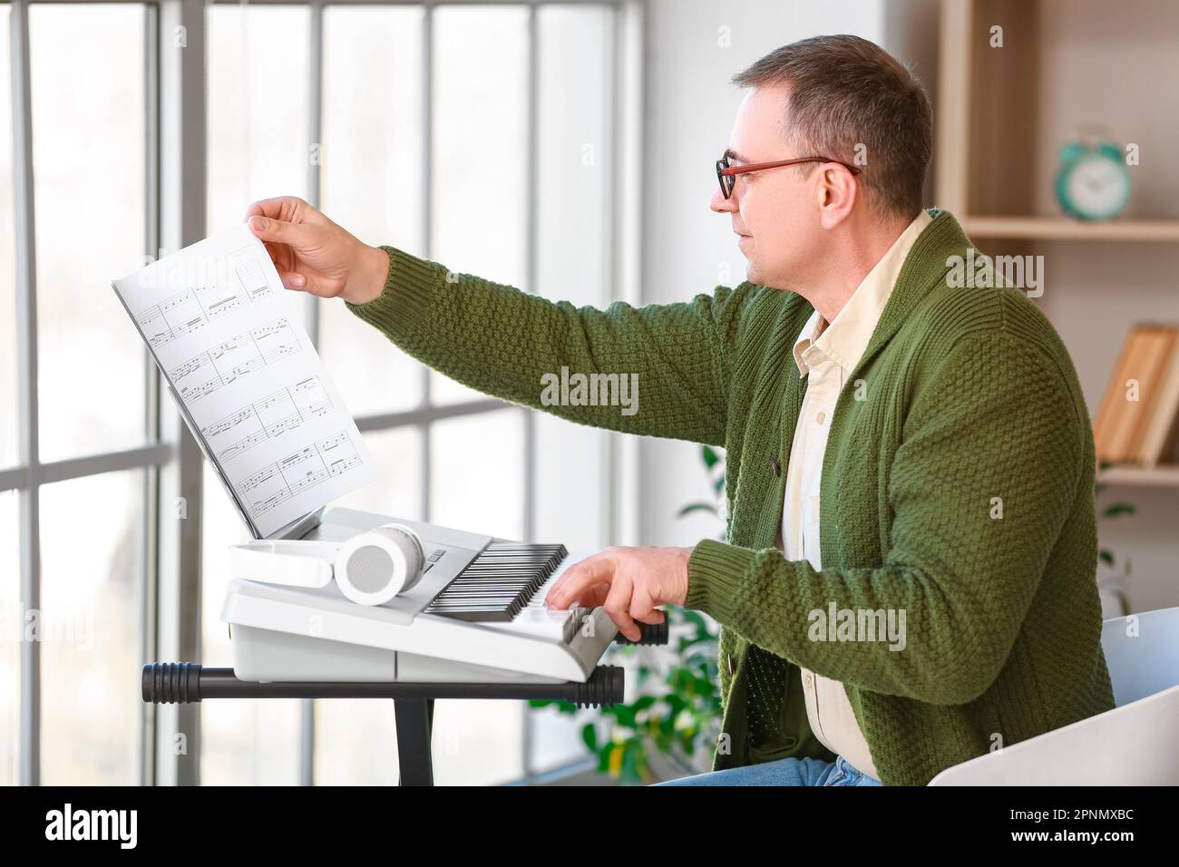 Mature man with note sheet playing synthesizer at home Stock Photo - Alamy