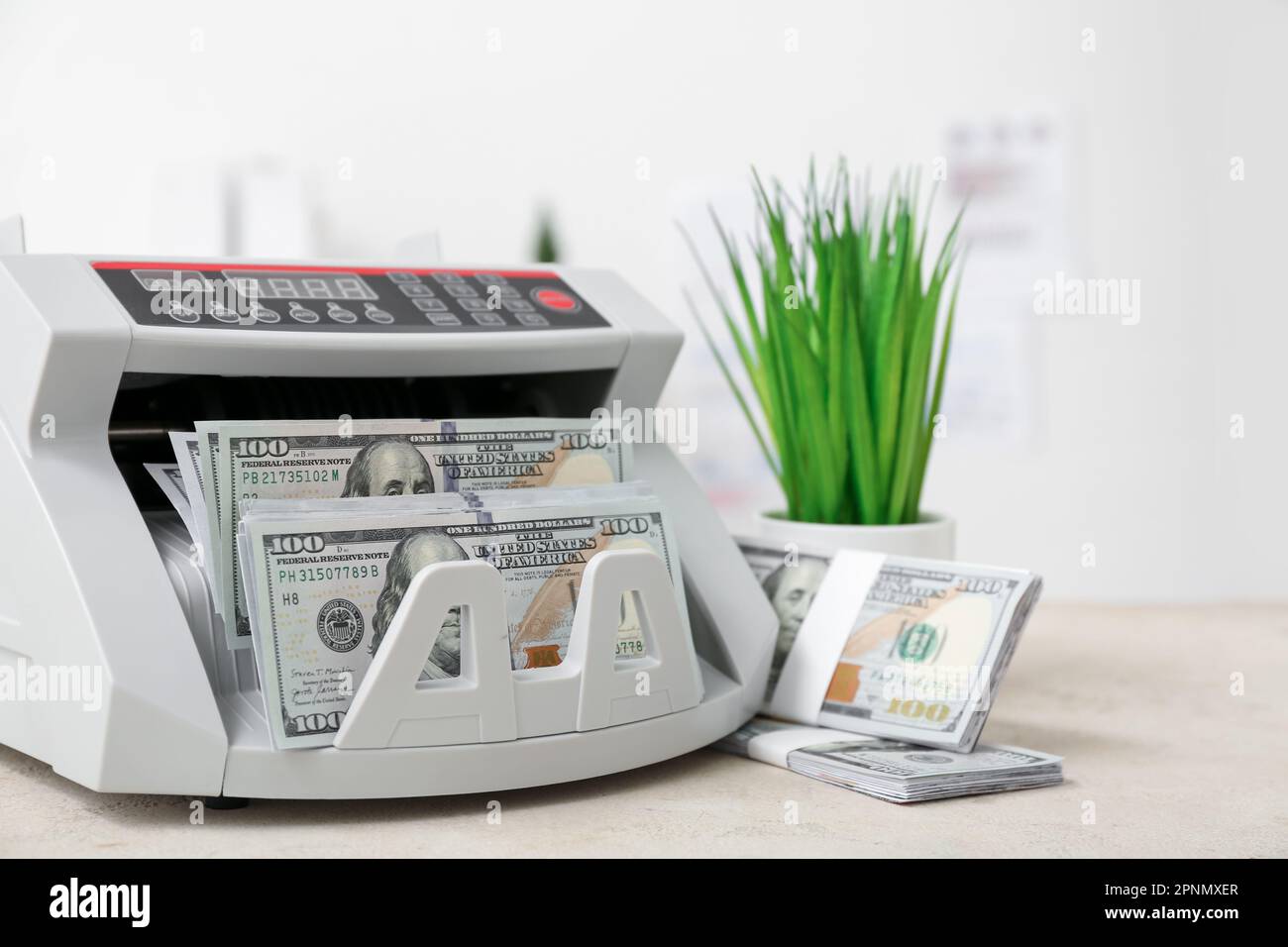 Modern cash counting machine with dollar banknotes and grass on table ...