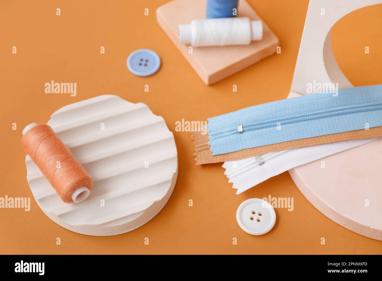 Podiums with thread spools, buttons and zips on orange background ...