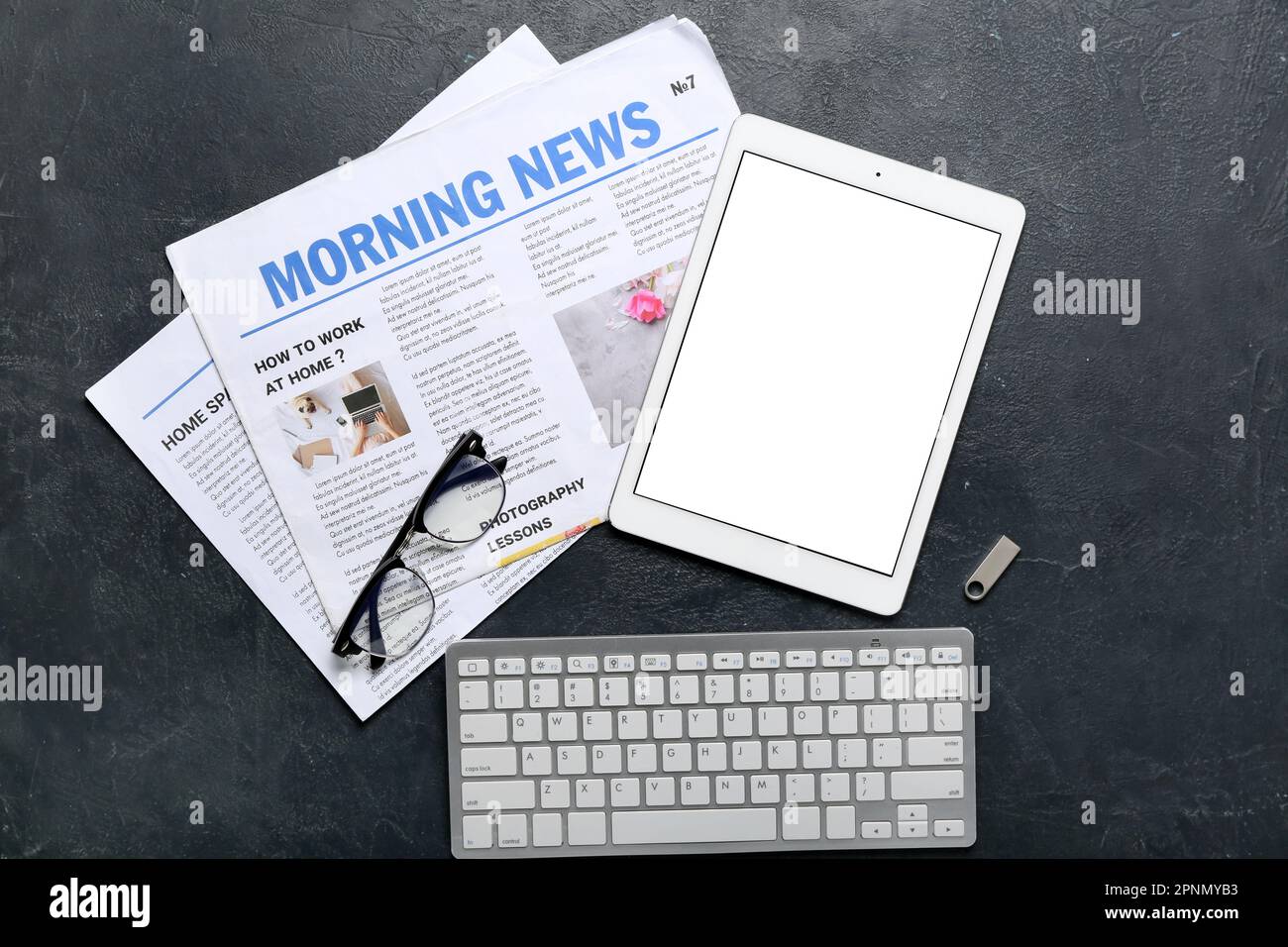 Tablet computer with newspapers, eyeglasses and keyboard on dark ...