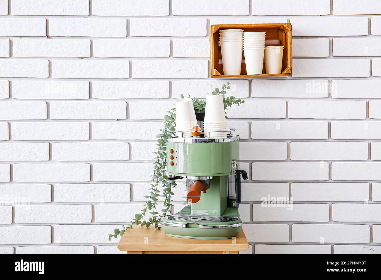 Modern coffee machine with paper cups and houseplant on table near white brick wall Stock Photo ...