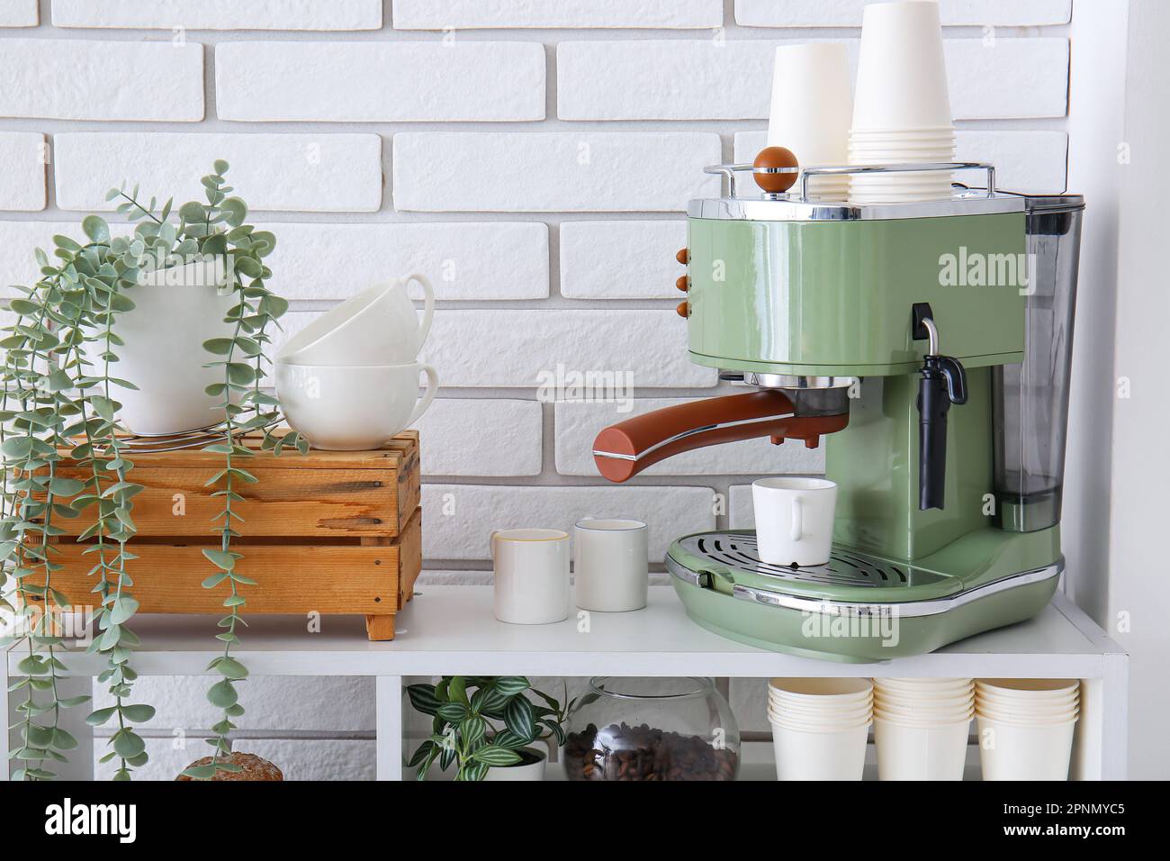 Modern coffee machine with cups and houseplants on shelving unit near ...