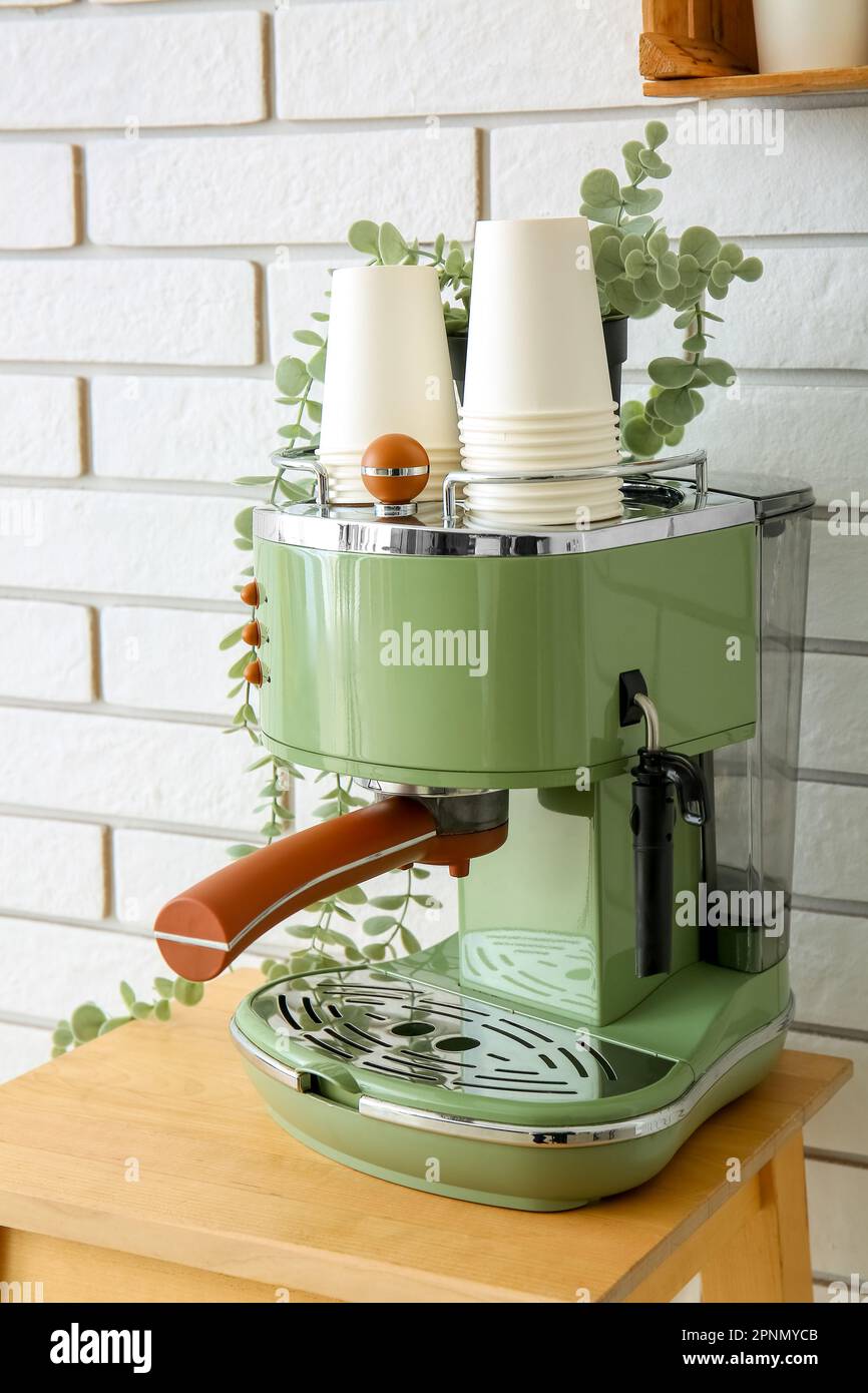 Modern coffee machine with paper cups and houseplant on table near ...