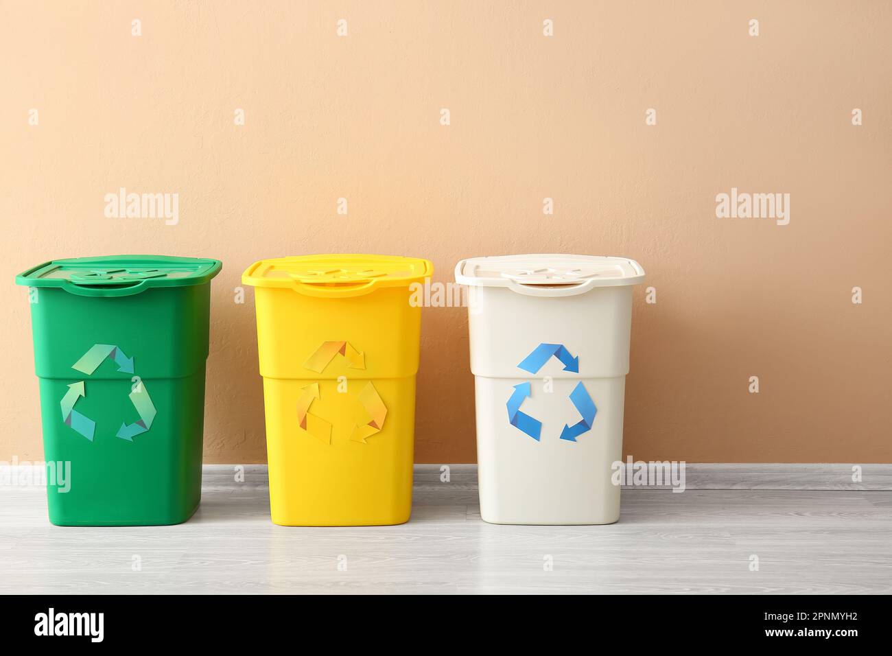 Different garbage bins with recycling symbol near beige wall Stock ...