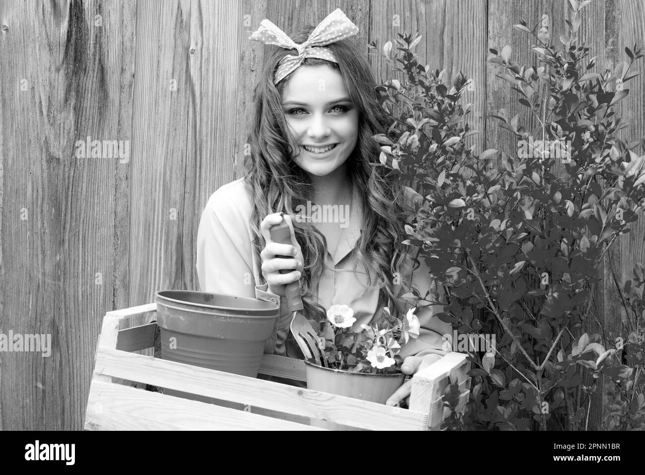 Planting flowers. Pretty smiling girl holding garden tools at wooden ...