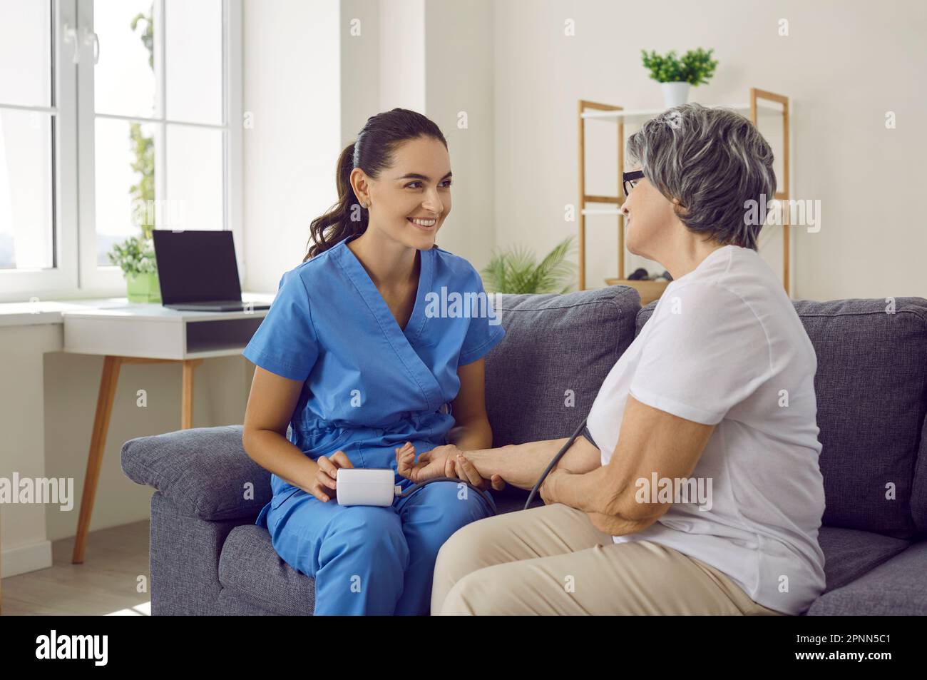 Smiling nurse measuring pressure of positive elderly woman Stock Photo ...