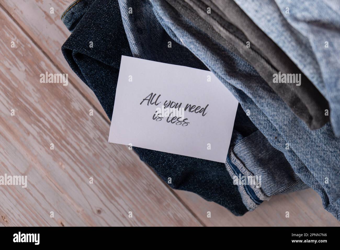 ALL YOU NEED IS LESS text on paper note on Jeans clothes assortment ...