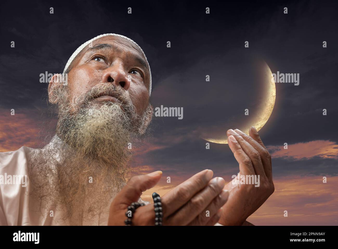 Muslim man with a beard wearing a white cap praying with prayer beads ...