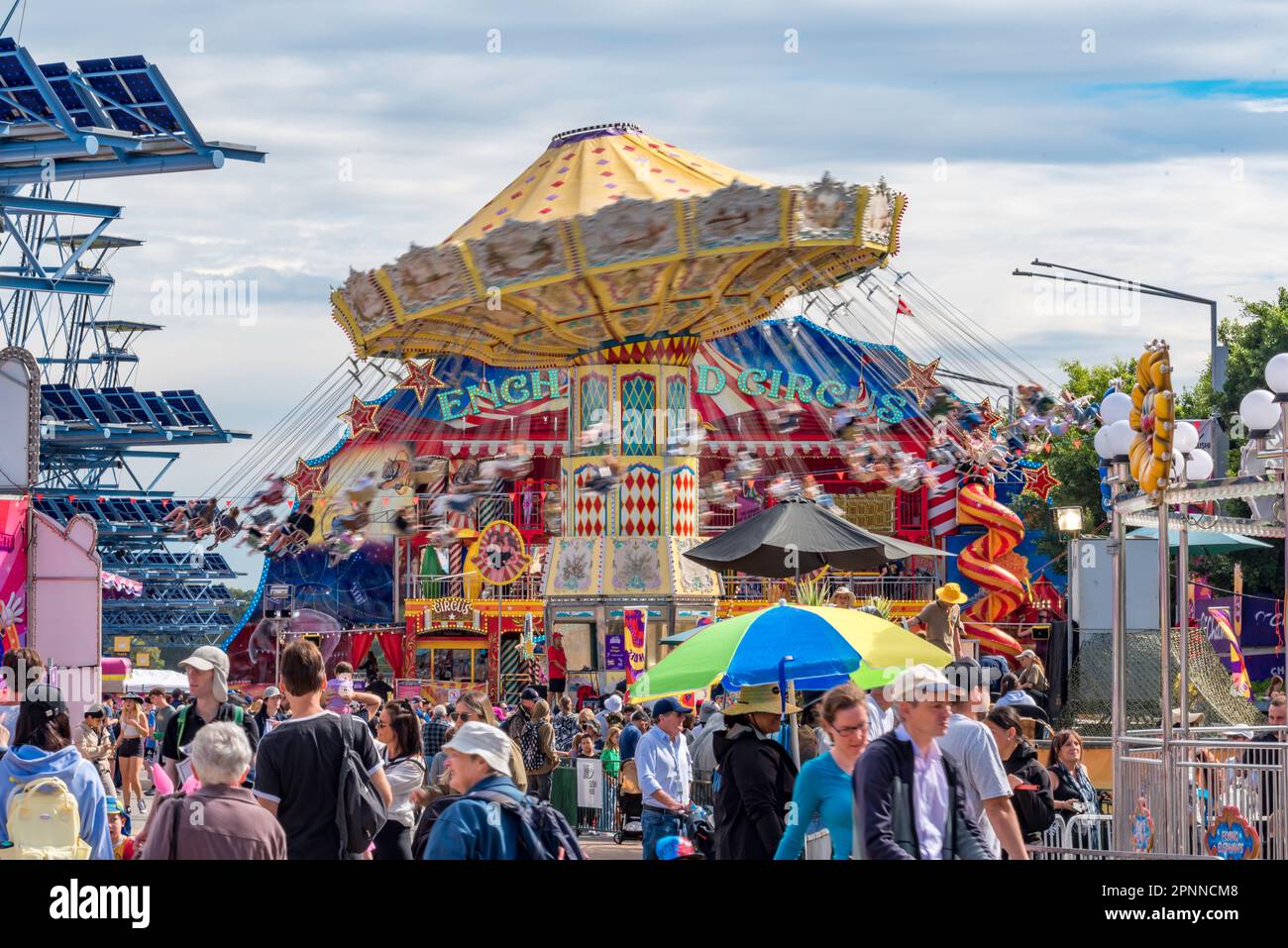 Crowds of people walk past and enjoy riding on the many fun and ...
