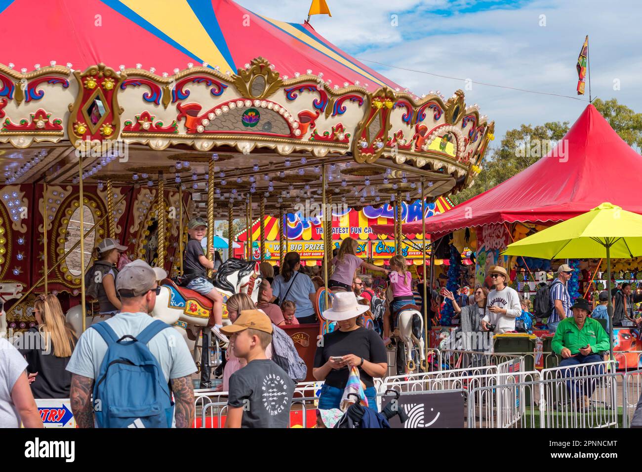 Crowds of people walk past and enjoy riding on the many fun and ...