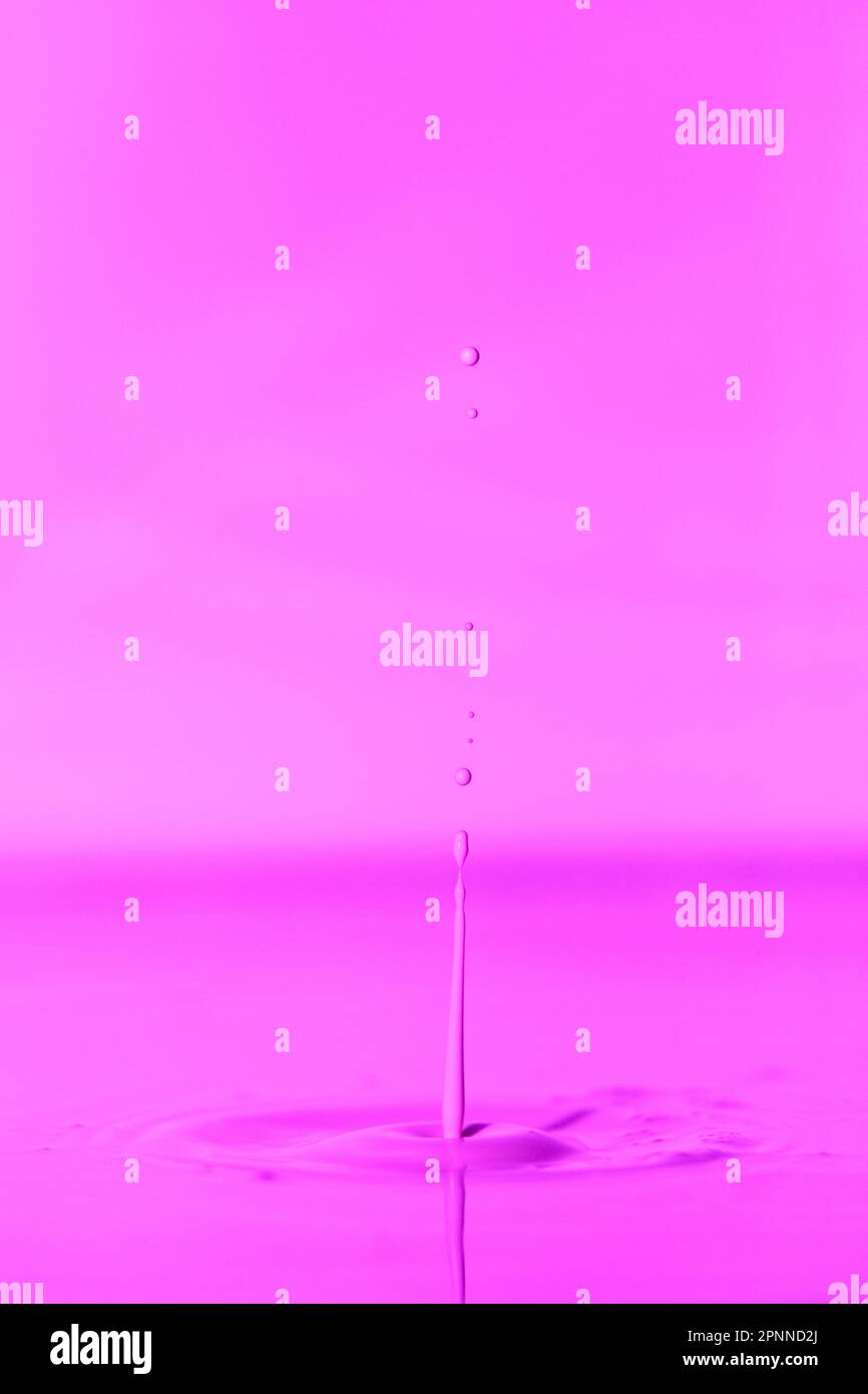 A drop falls into a thick liquid with a pink background. Abstract ...
