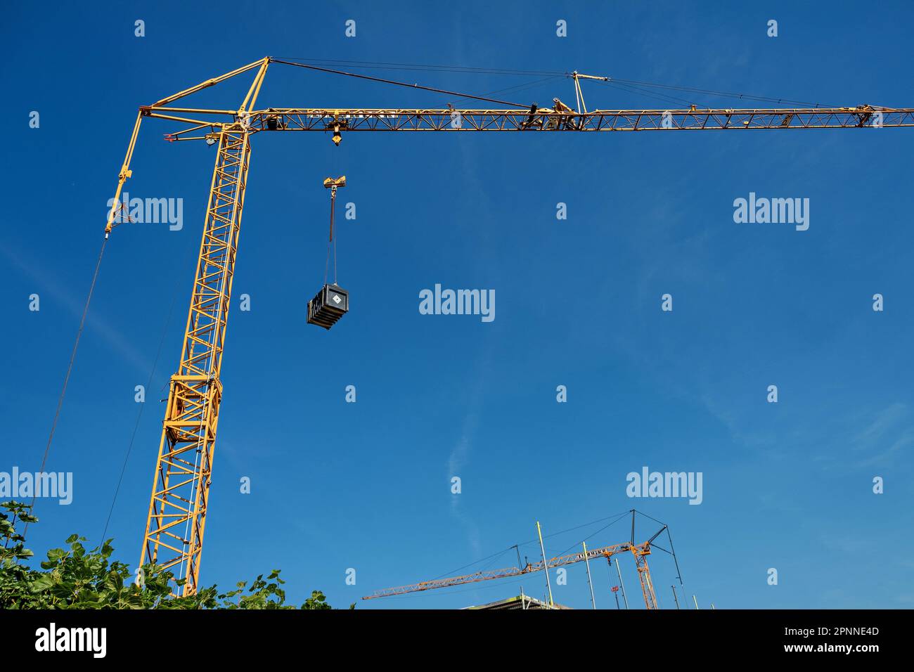 A tall yellow construction crane with a dangling black box against a ...