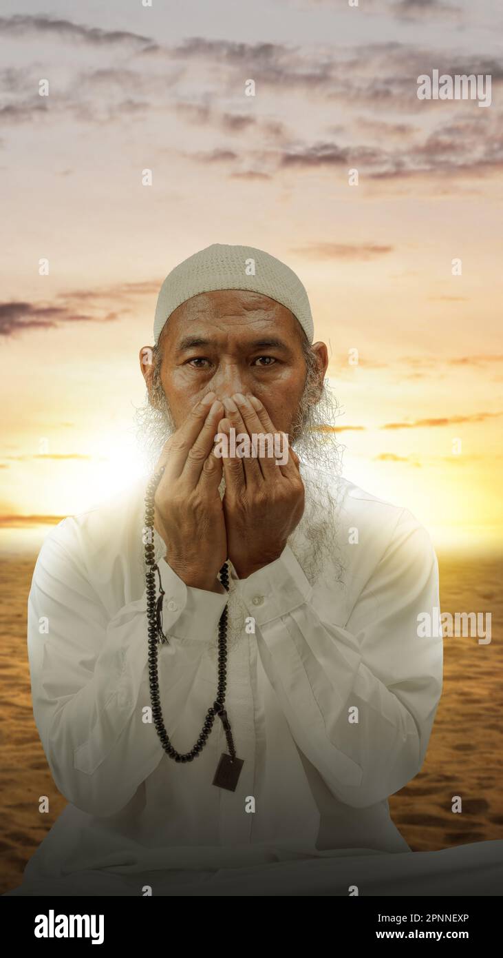 Muslim man with a beard wearing a white cap praying with prayer beads ...