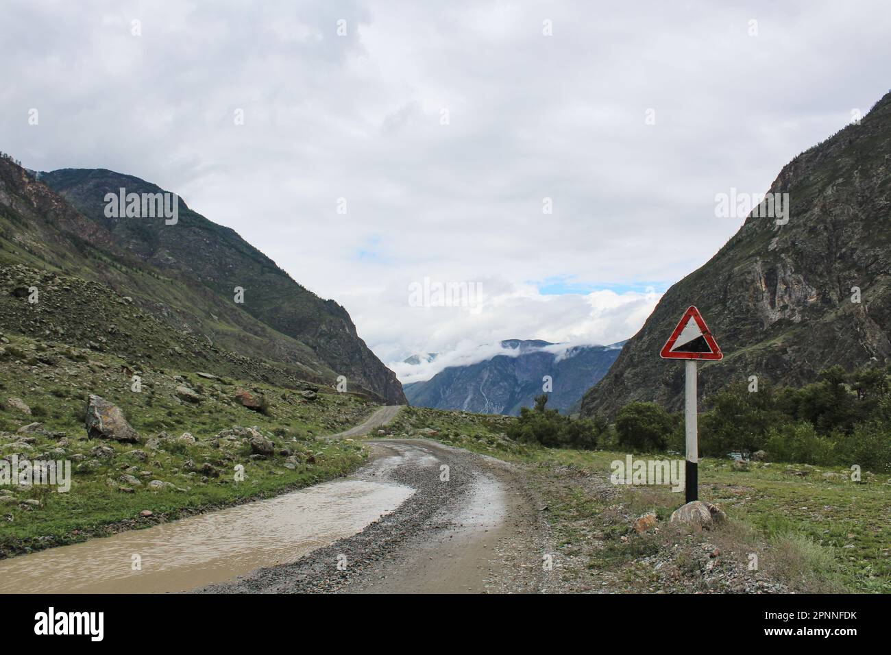 road sign indicating a slope on a wet dirt mountain road after rain ...