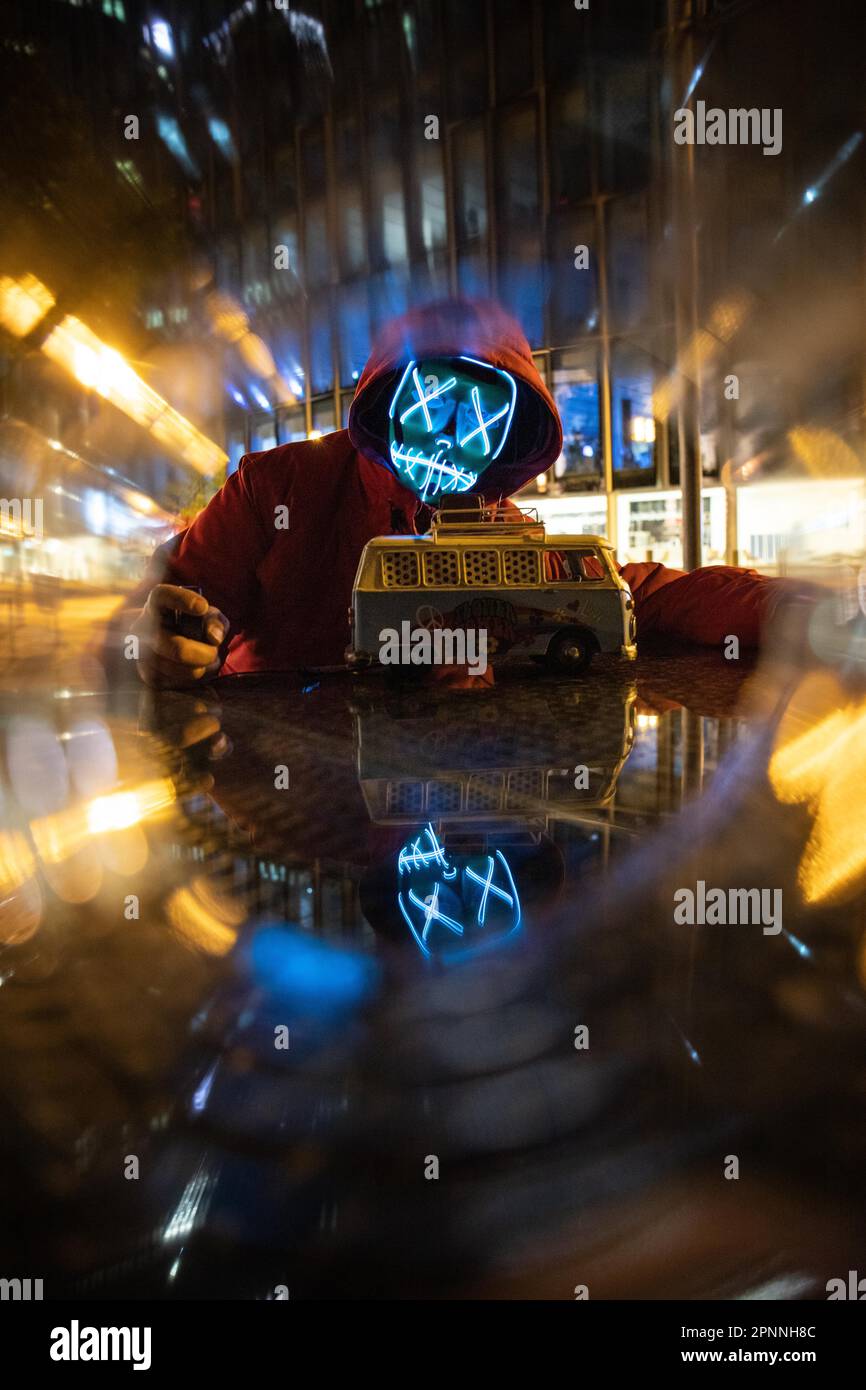 Purge mask, man in red jacket with LED mask. At night, city lights ...