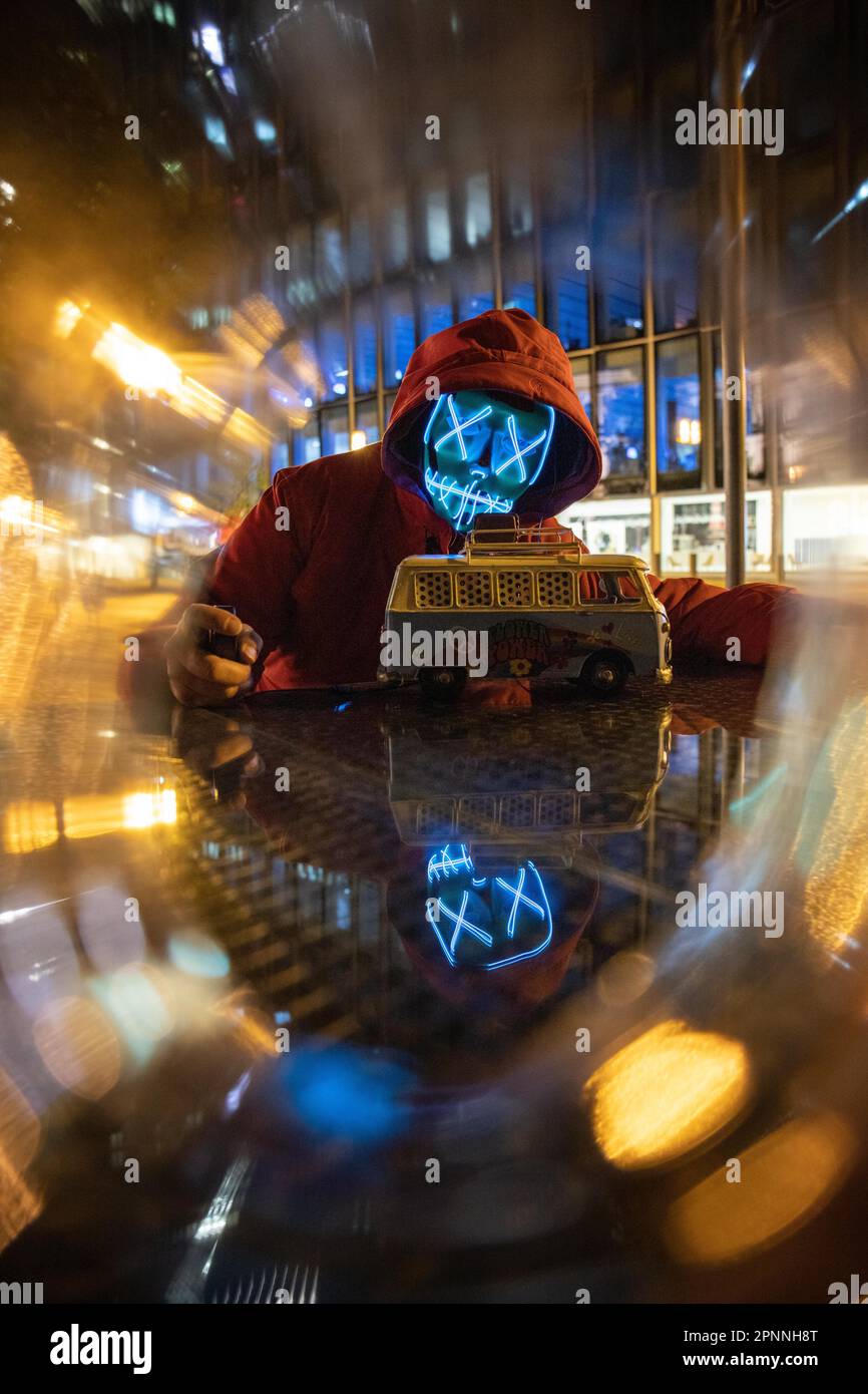 Purge mask, man in red jacket with LED mask. At night, city lights ...