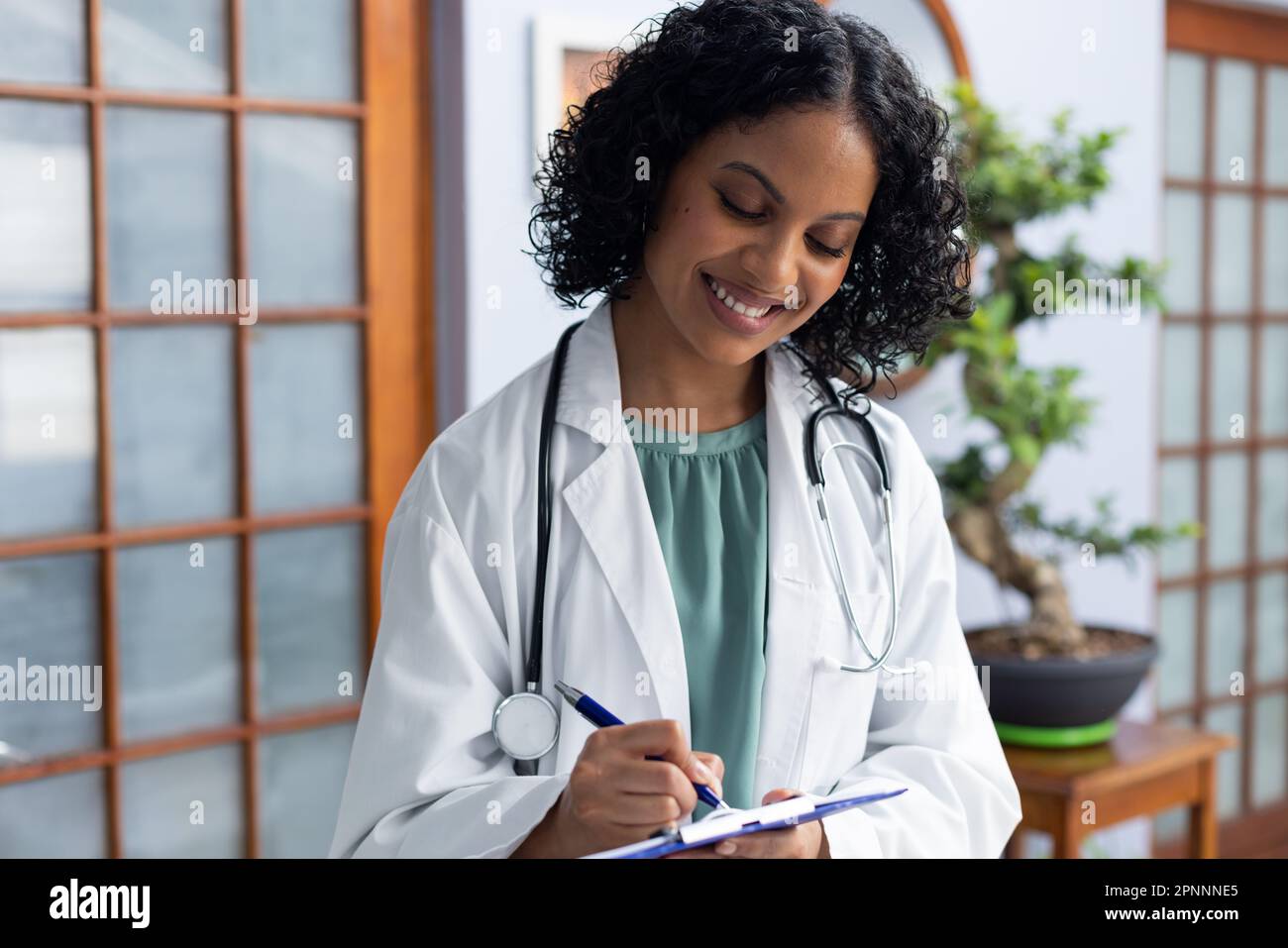 Happy biracial female doctor holding clipboard and taking notes at ...