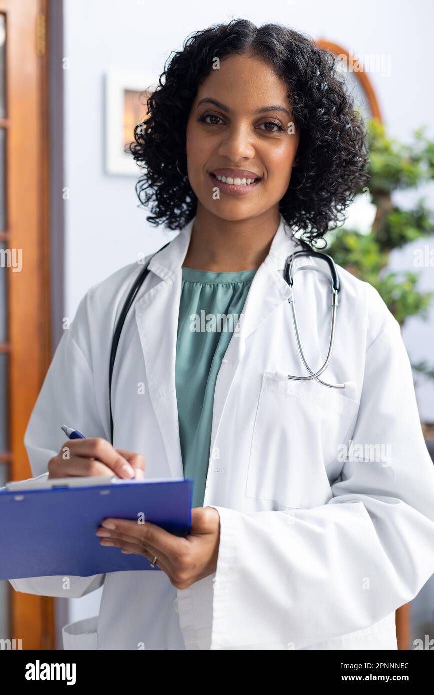 Portrait of happy biracial female doctor holding clipboard and smiling ...