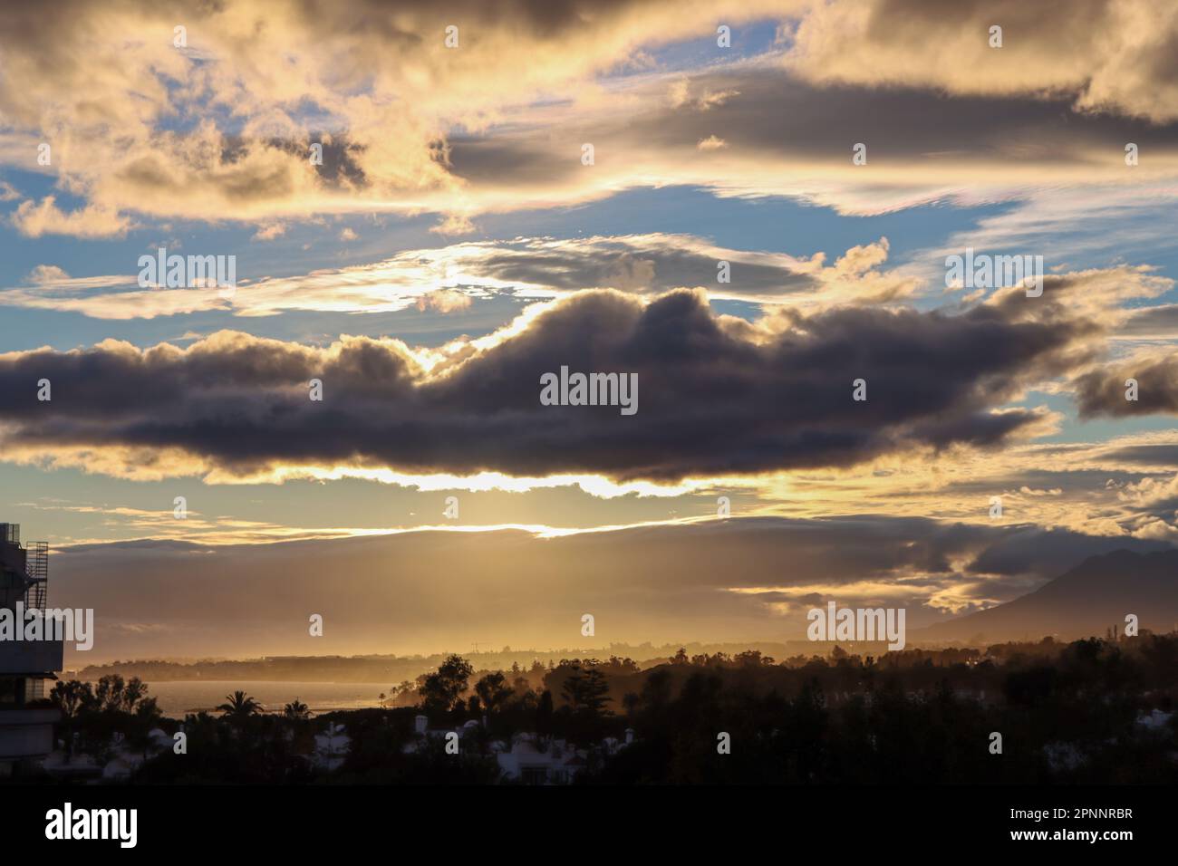 sun rising behind white clouds with buildings Stock Photo - Alamy
