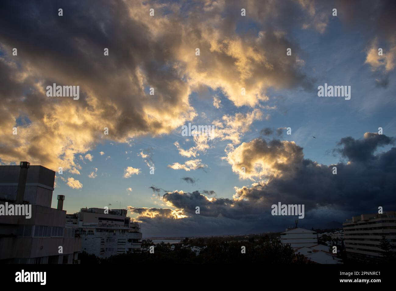 sun rising behind white clouds with dark buildings Stock Photo - Alamy