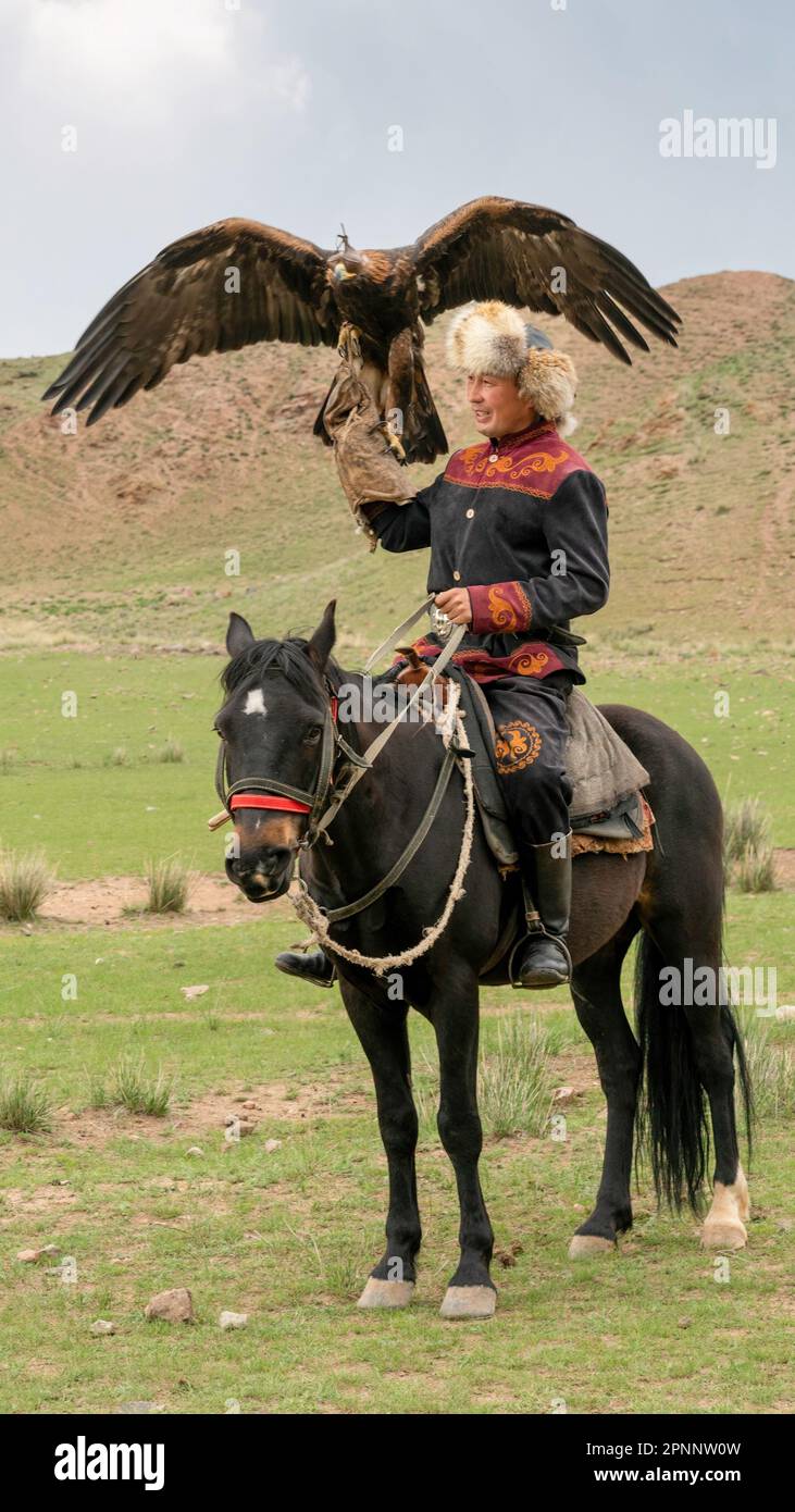 Issyk Kul, Kyrgyzstan - May 2022: Eagle trainer on a horse and his golden eagle, skilled in ...
