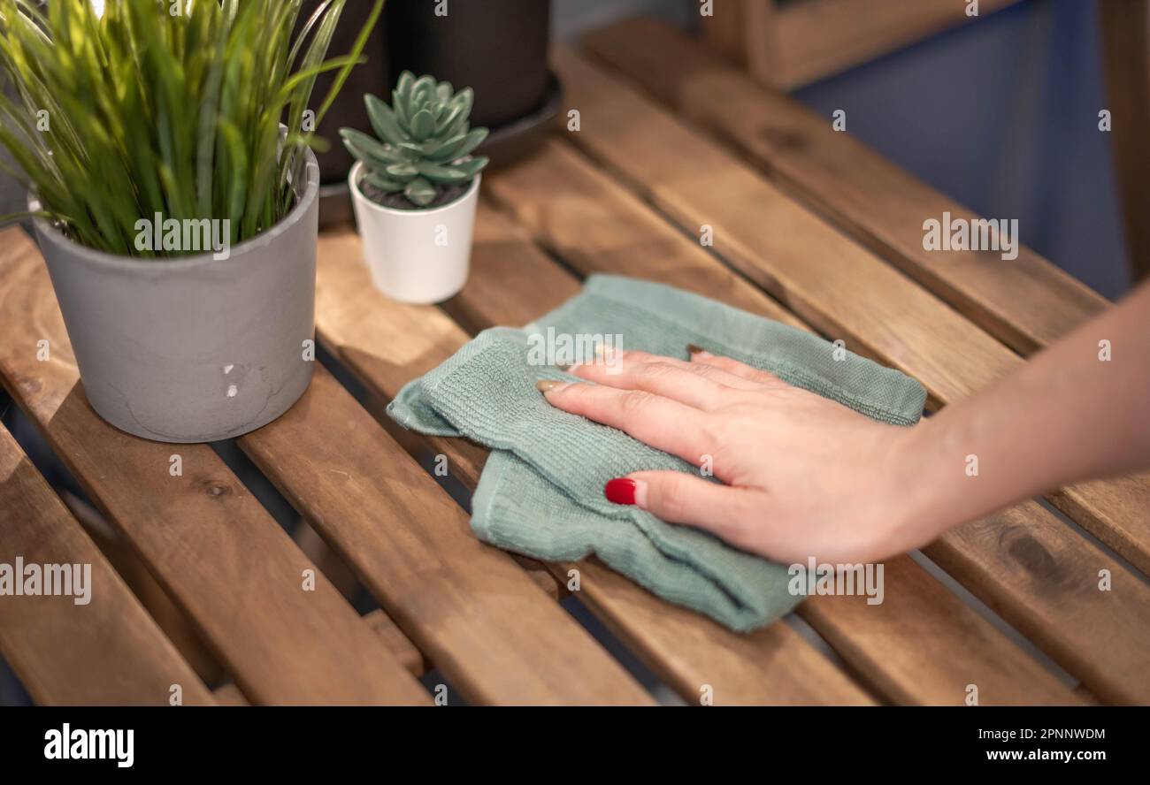 Close-up female hand cleaning wooden table using disinfectant green ...