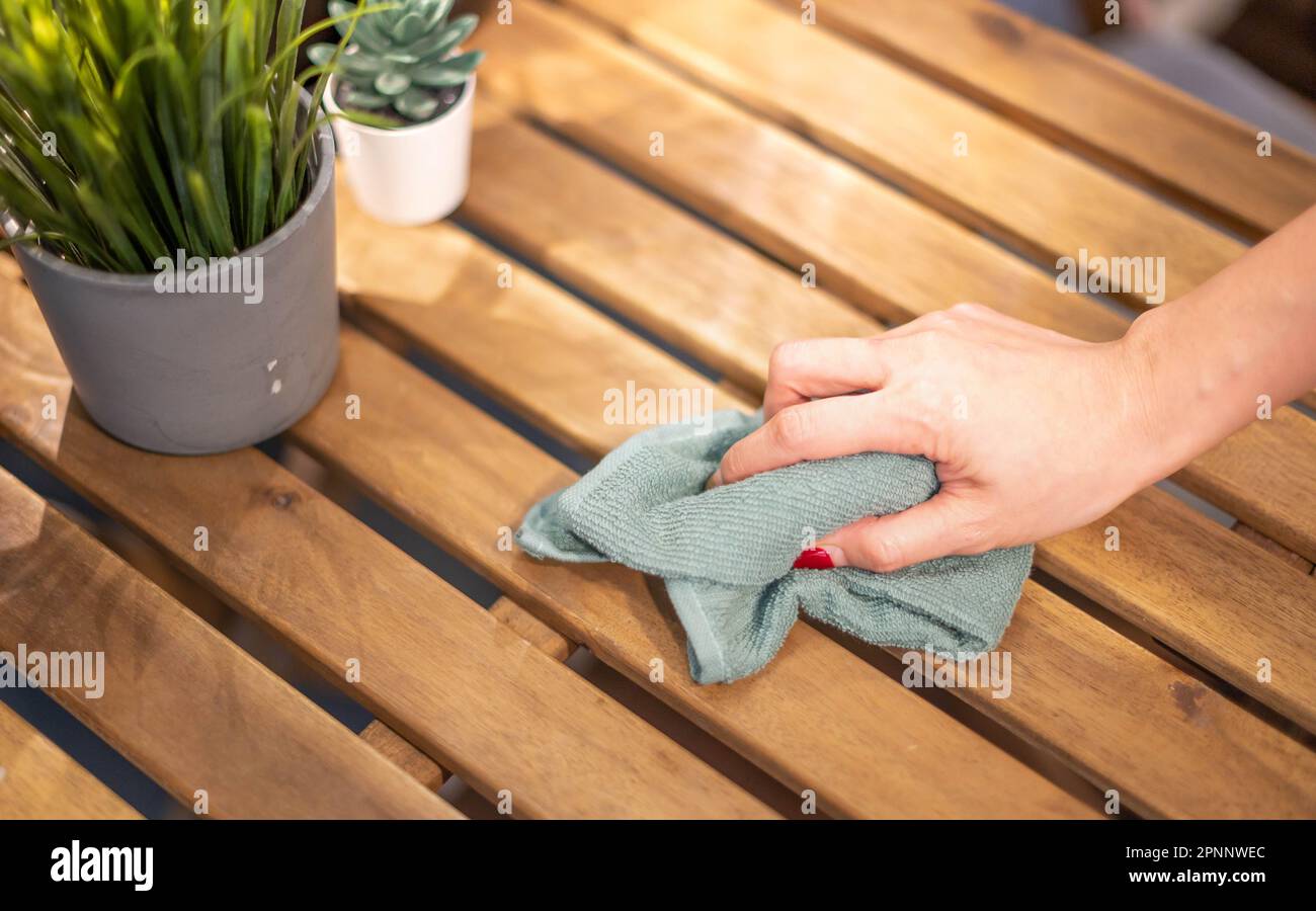 Close-up female hand cleaning wooden table using disinfectant green ...