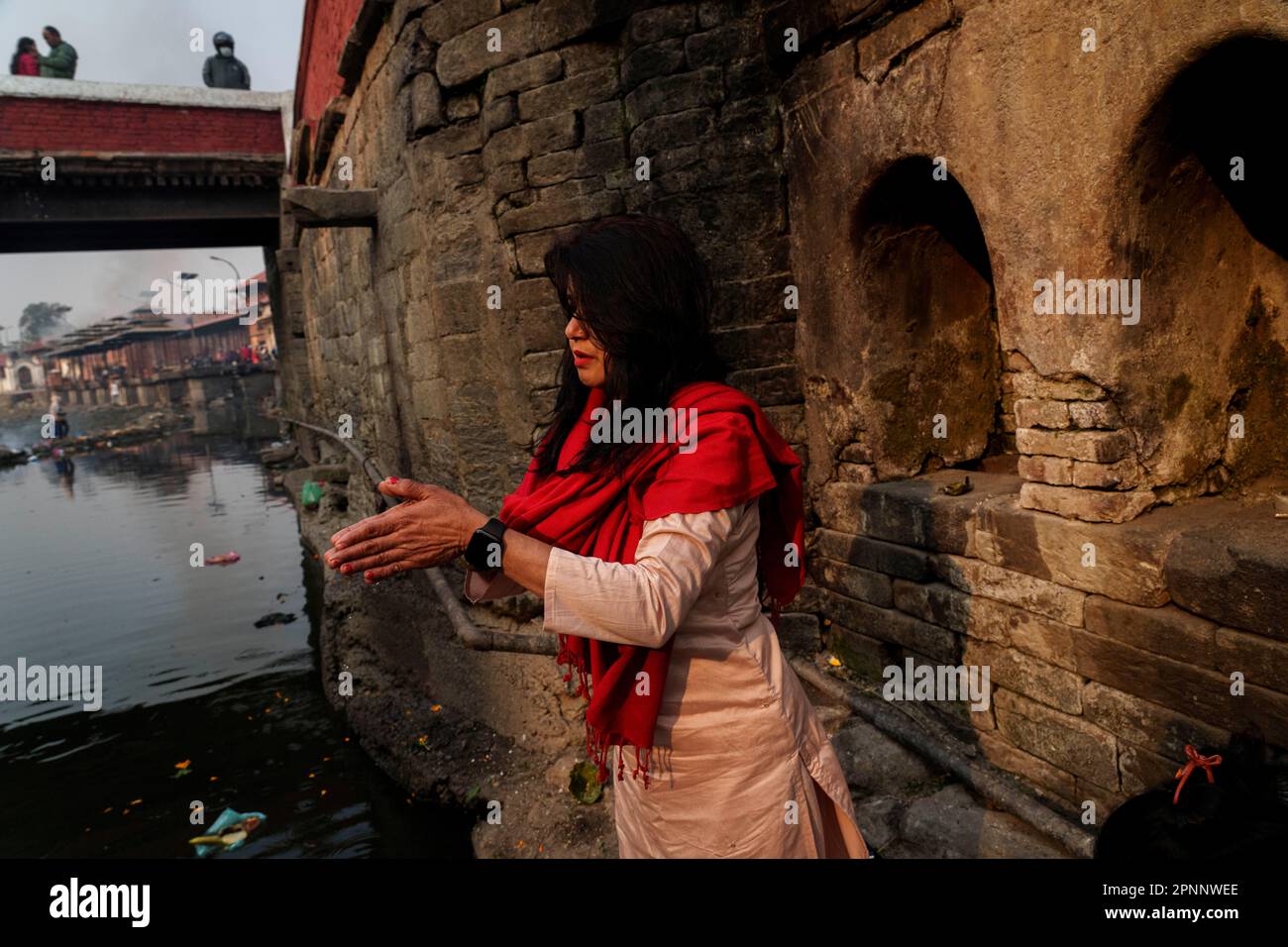 A Hindu devotee stands on the banks of the Bagmati river and offers ...
