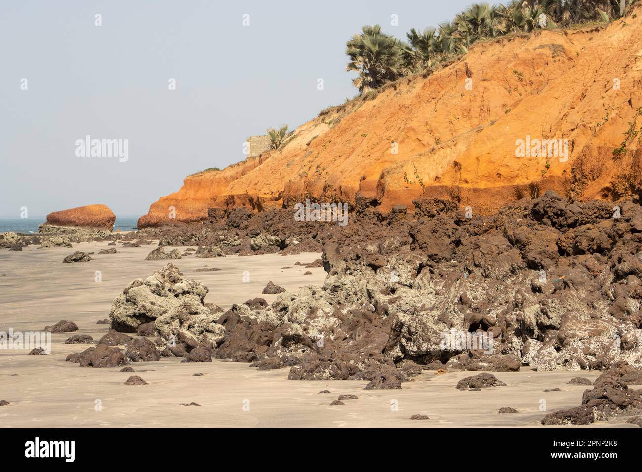 sloping tropical beach with orange cliffs and volcanic rock Stock Photo ...
