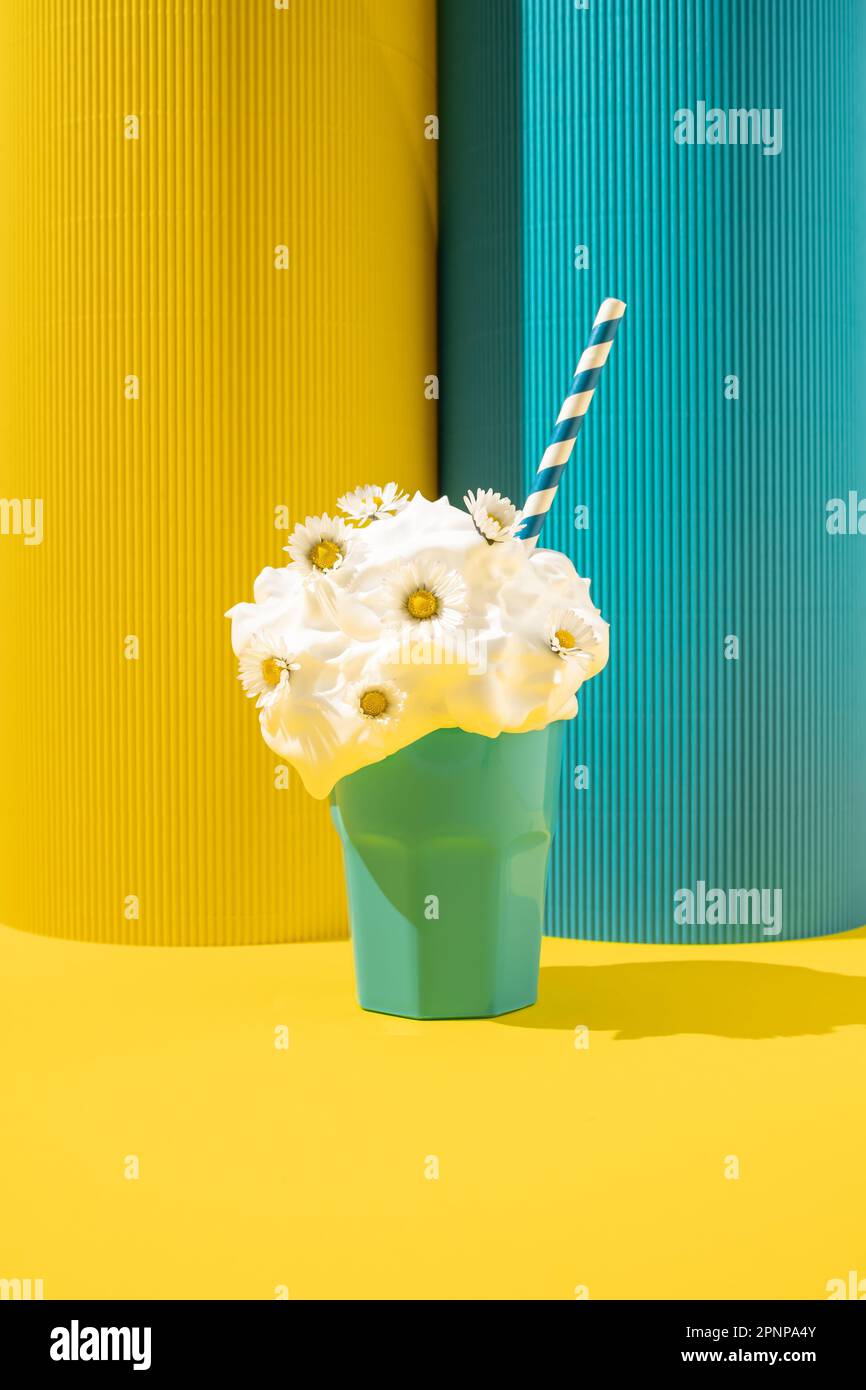 Creamy milkshake with daisy flowers and paper straw on yellow and blue ...